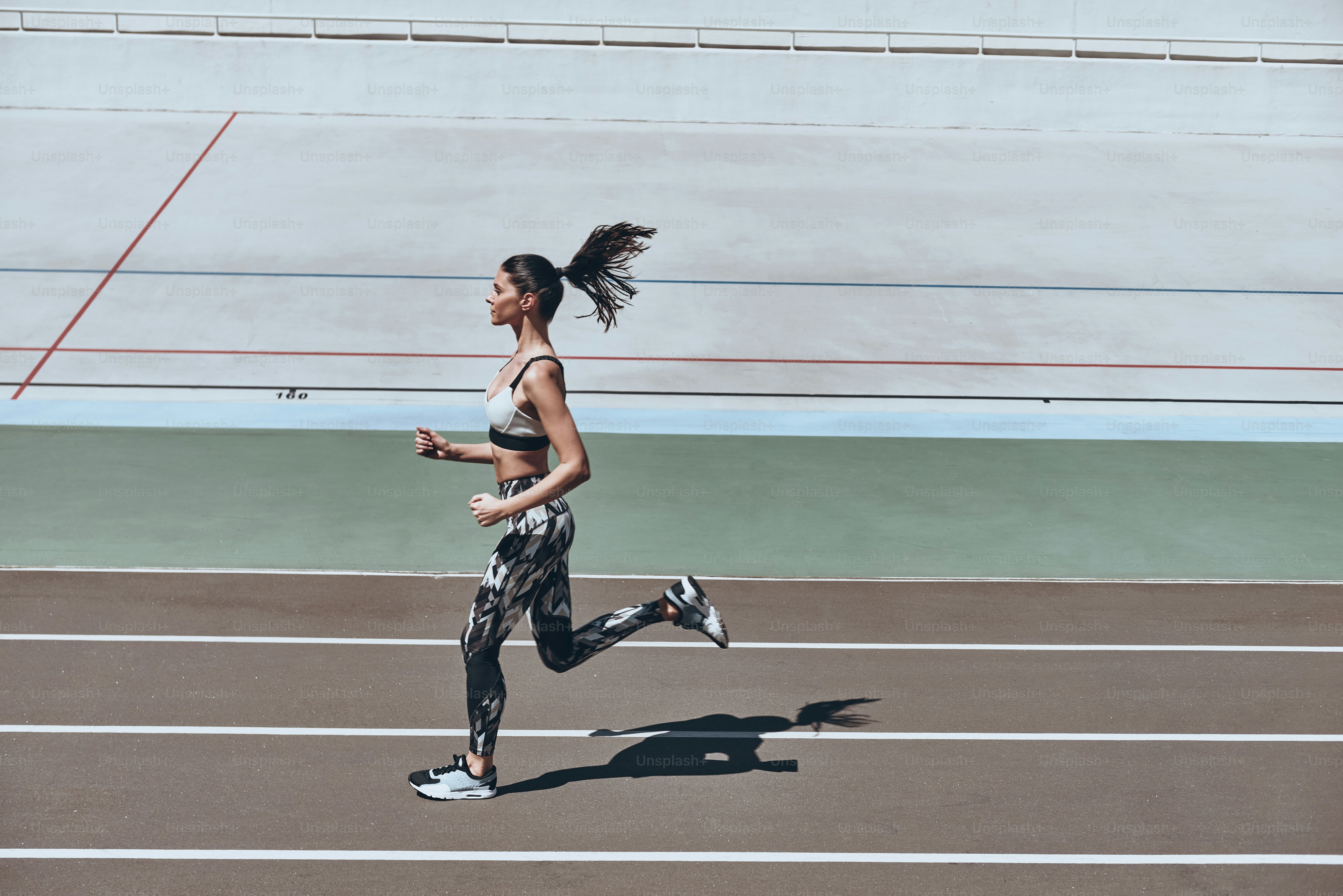 Full length of young woman in sports clothing running while exercising ...