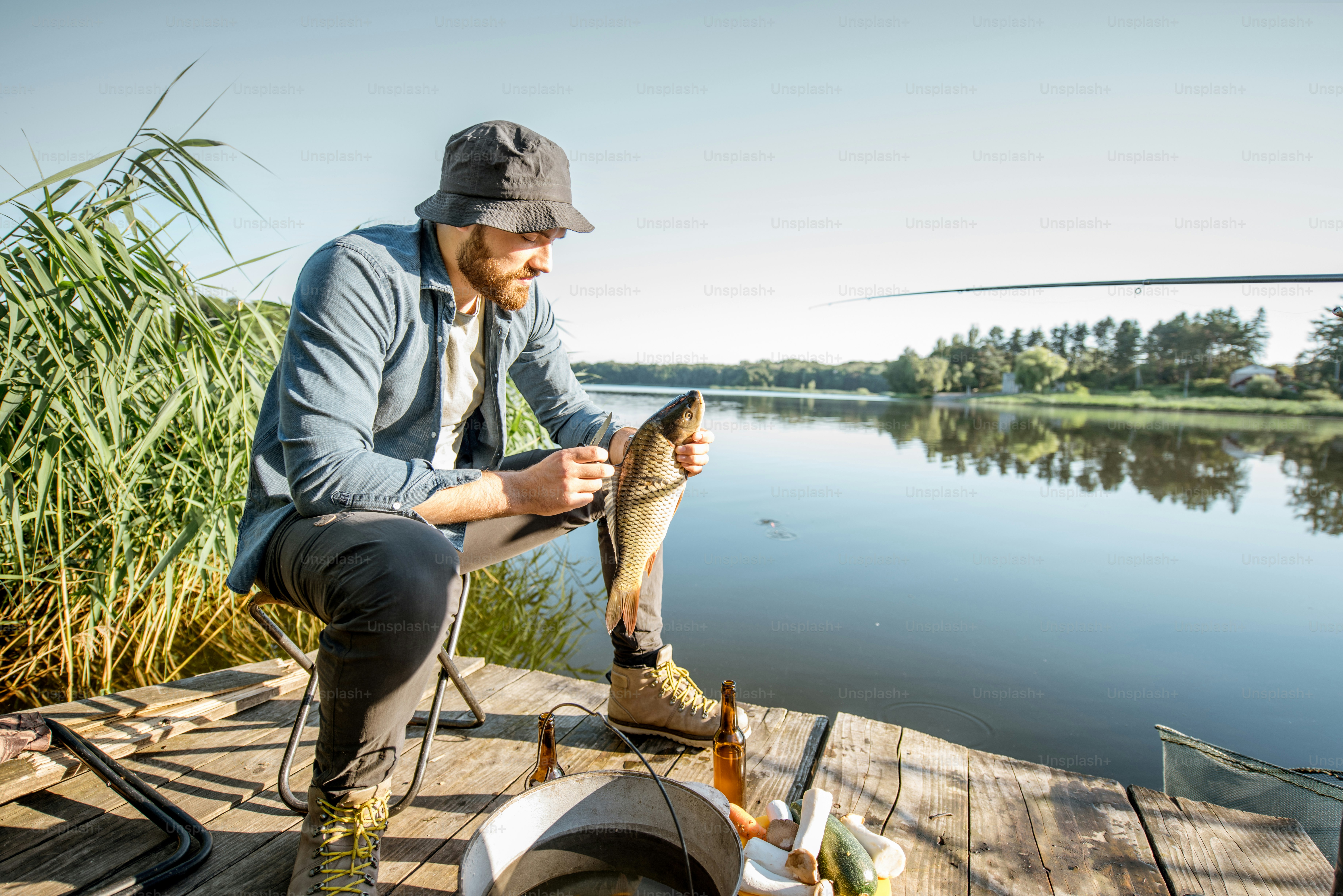 Portrait of a handsome fisherman with fish on the wooden pier near the ...