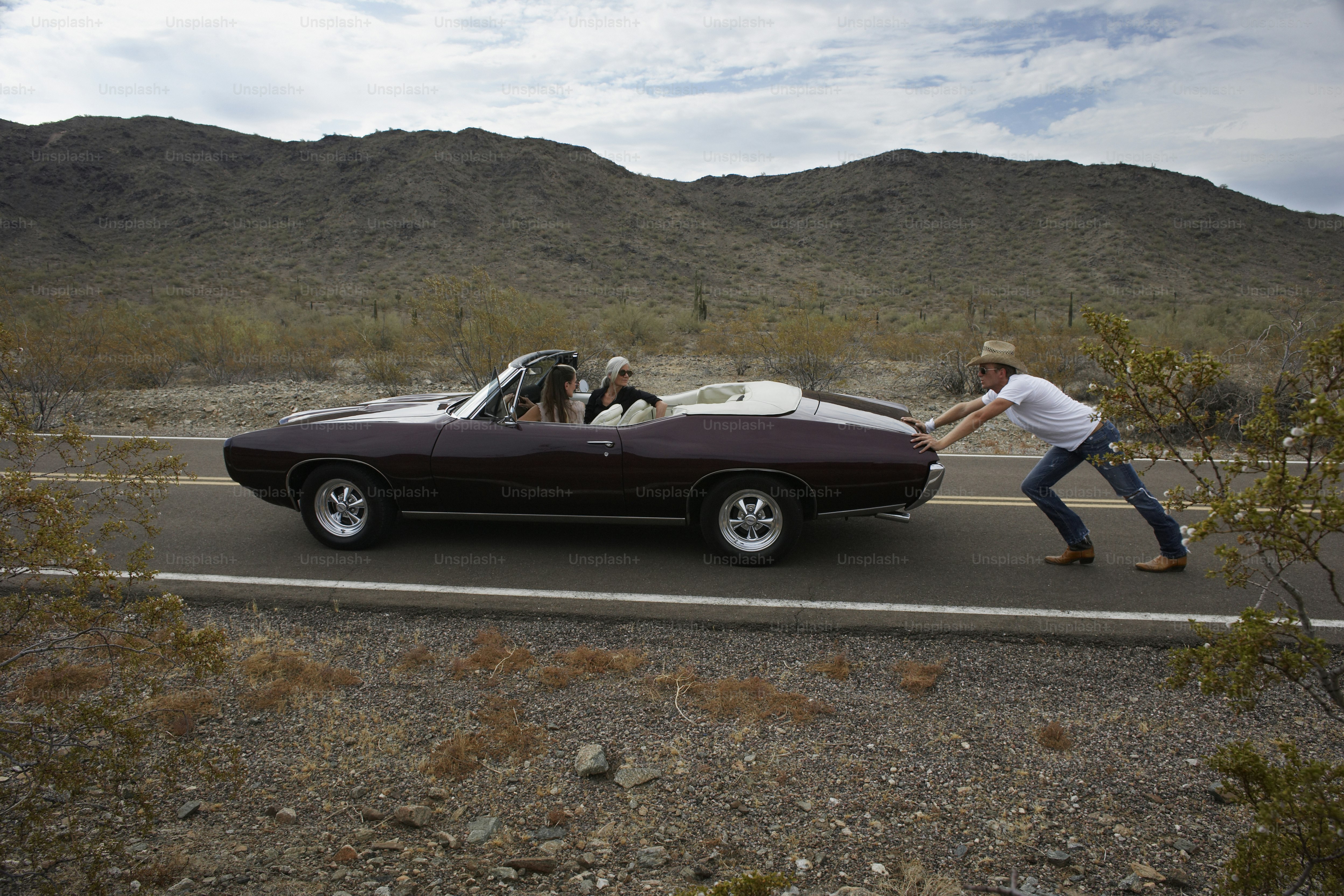 A man pushing a convertible car down the road photo – Pushing Image on ...