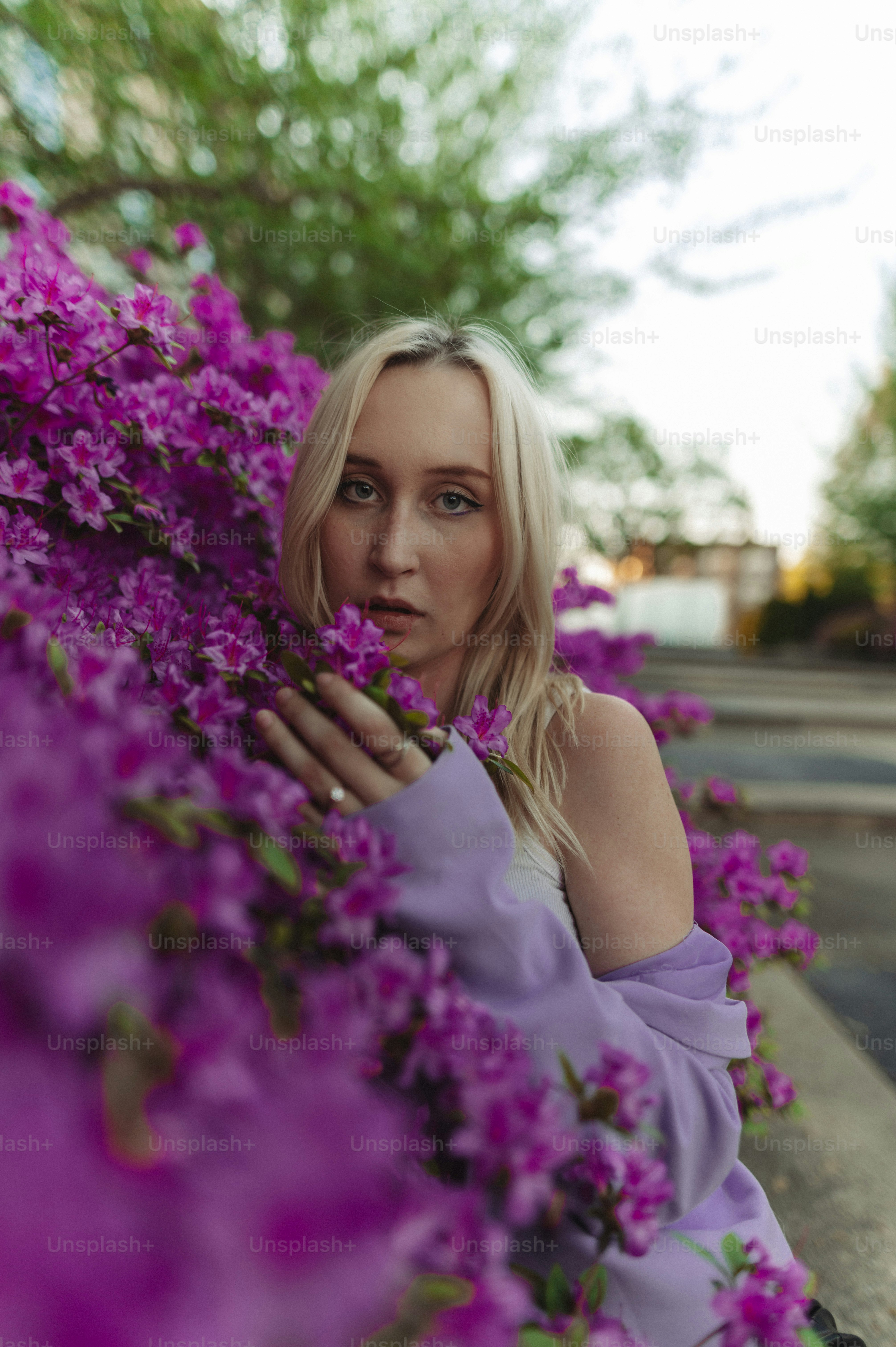 A woman in a purple dress leaning against a bush of purple flowers ...