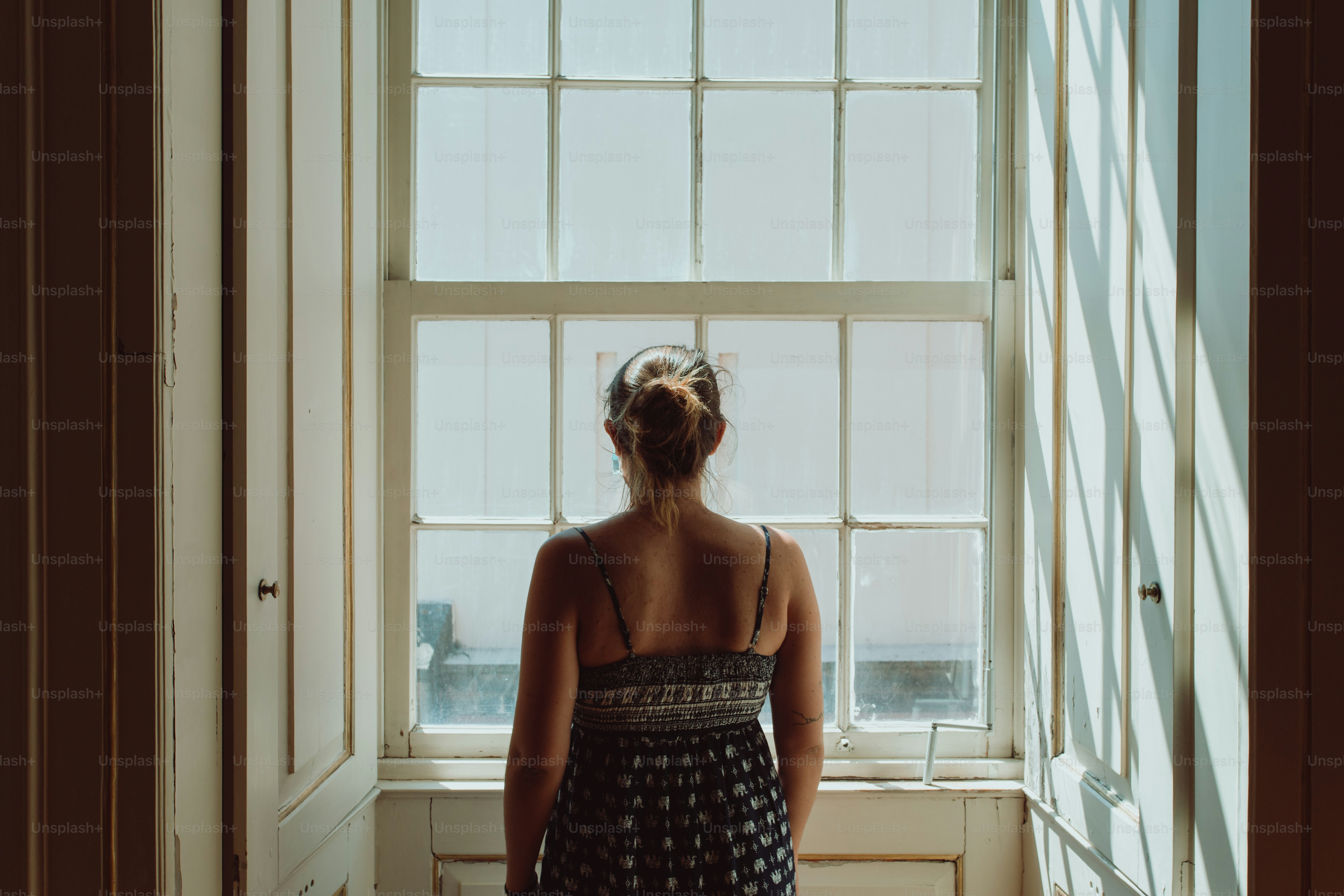 A woman standing in front of a window looking out photo – Insecurity ...