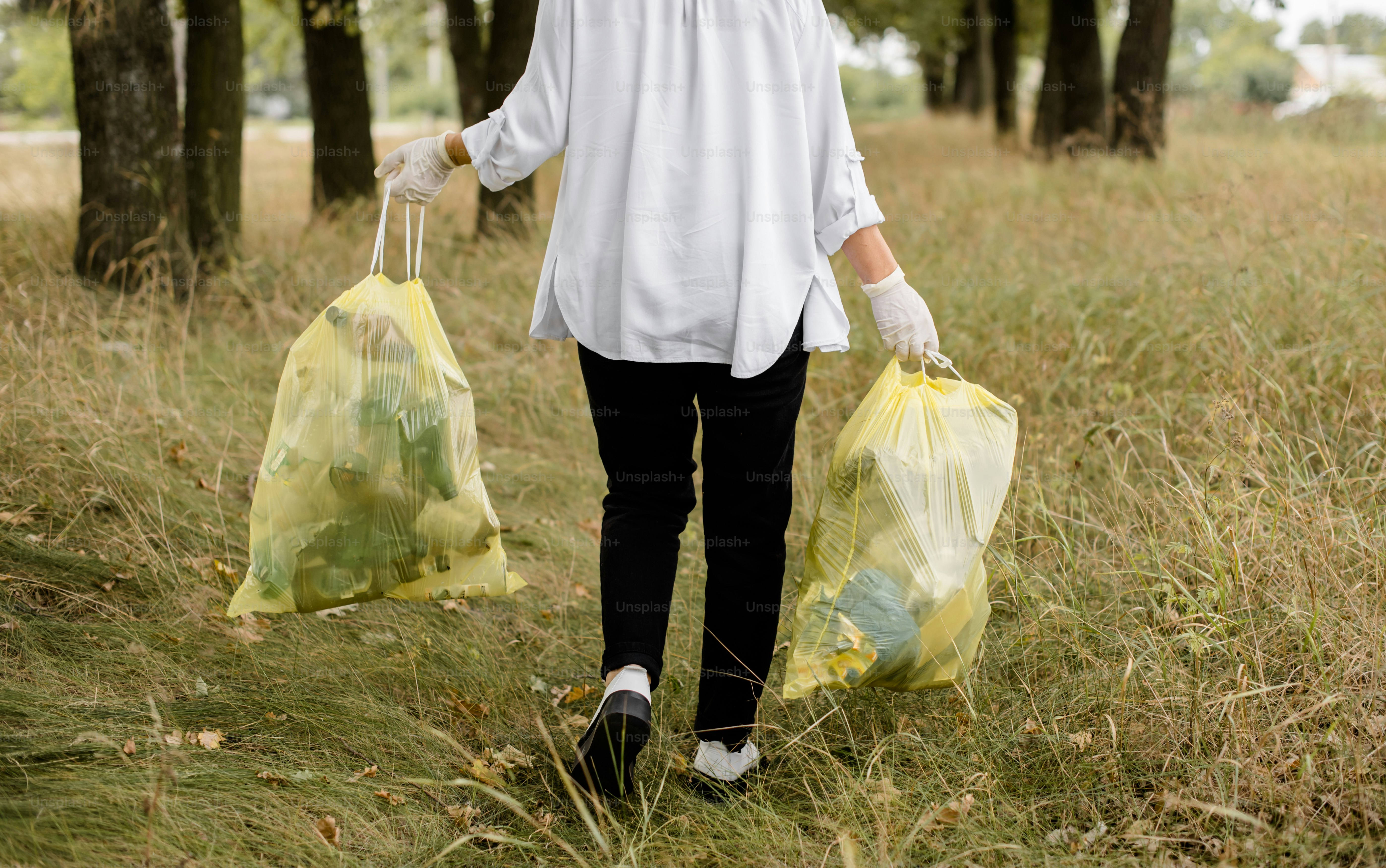 A woman walking through a field carrying two bags photo – Garbage Image ...