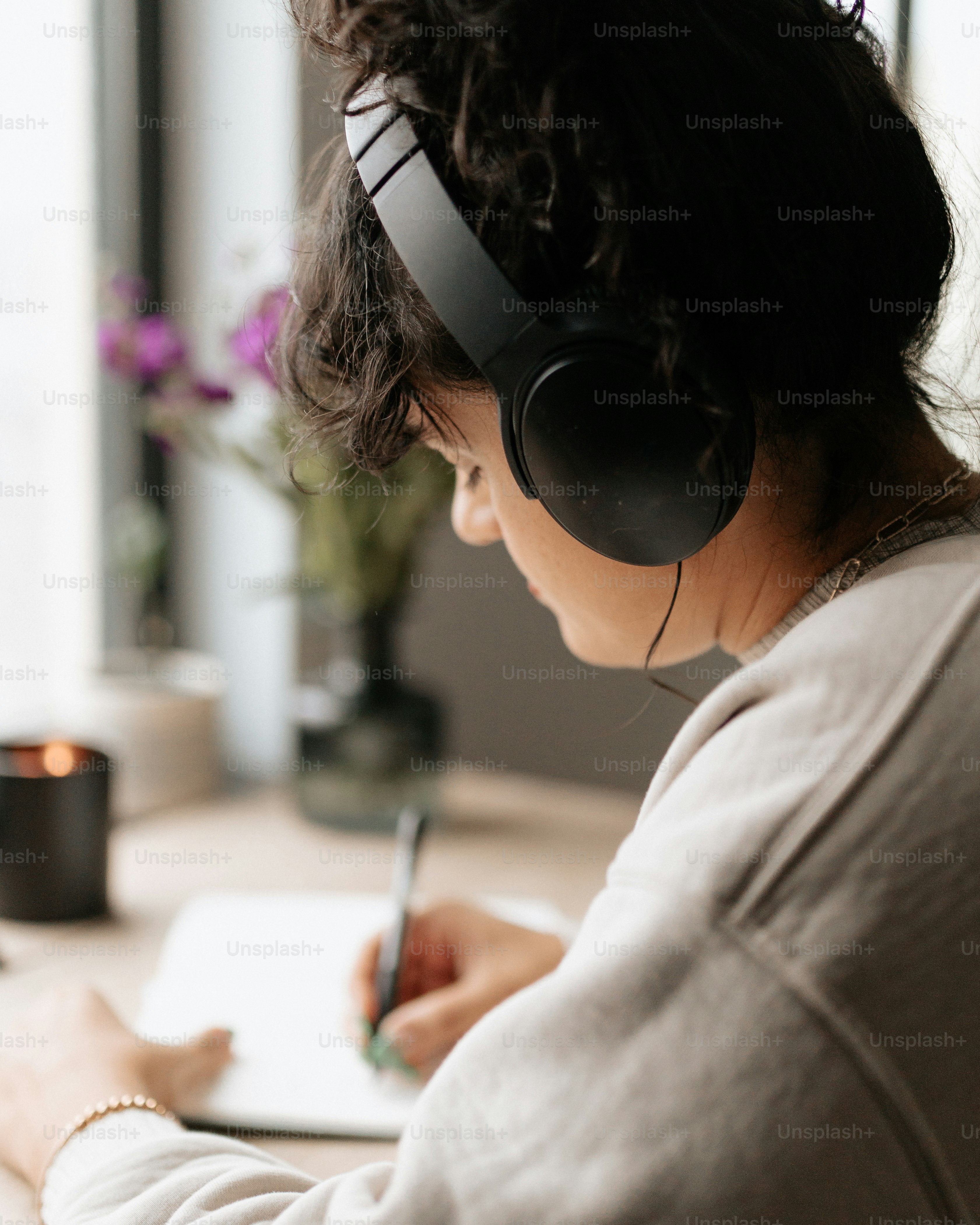 A woman wearing headphones writing on a notepad photo – Article writing ...