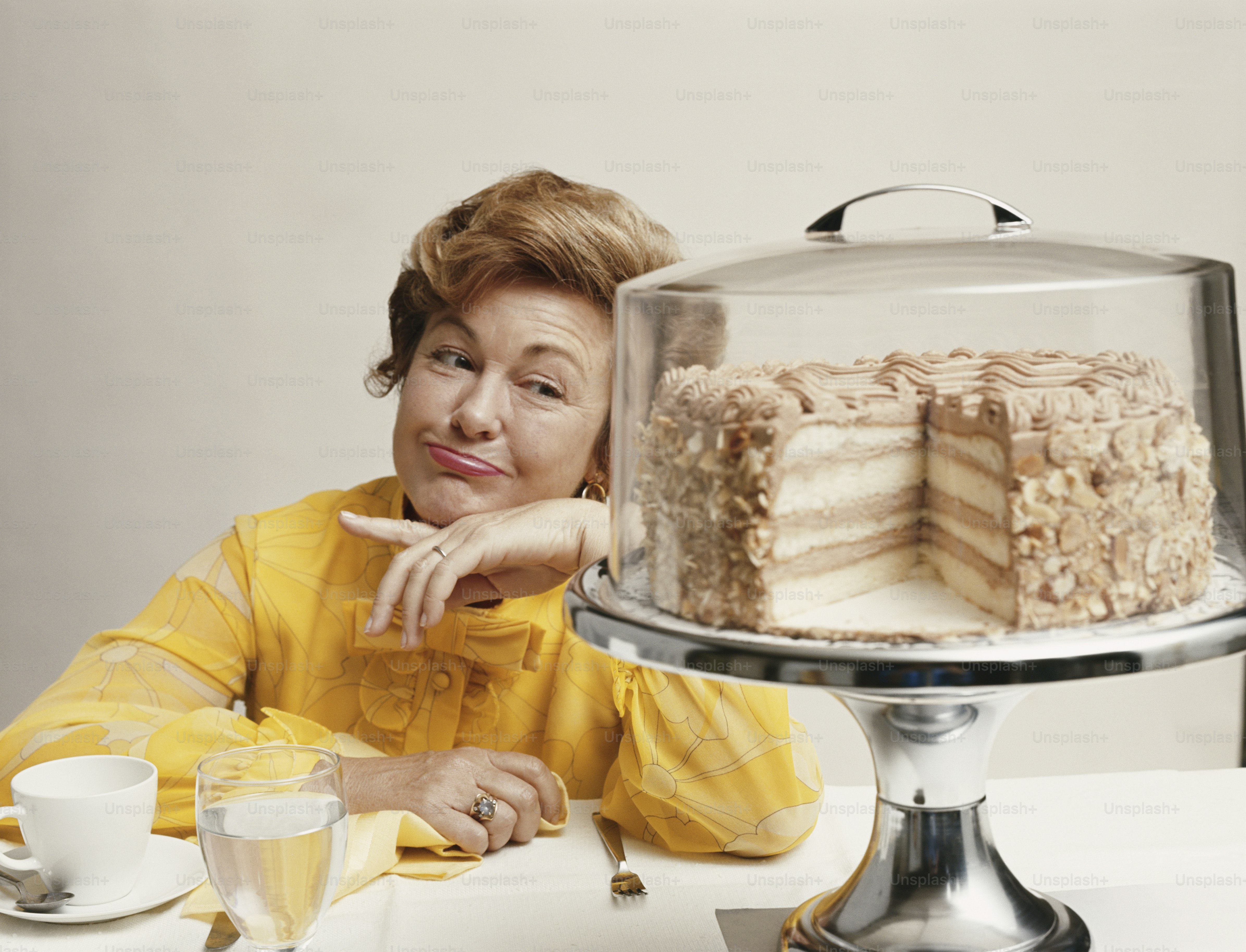 A woman sitting in front of a cake on a table photo – Layer cake Image ...