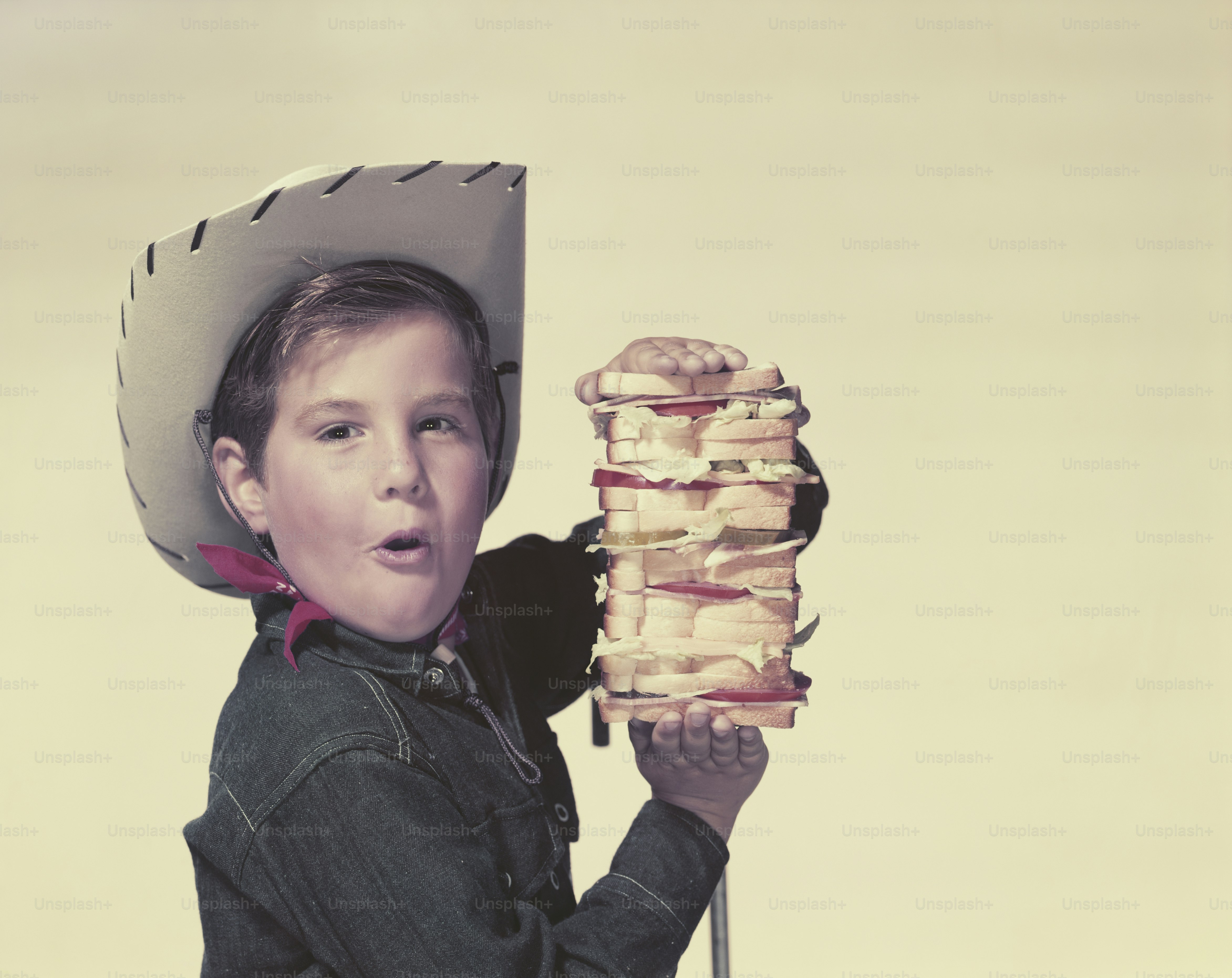 A young boy wearing a cowboy hat holding a stack of sandwiches photo ...