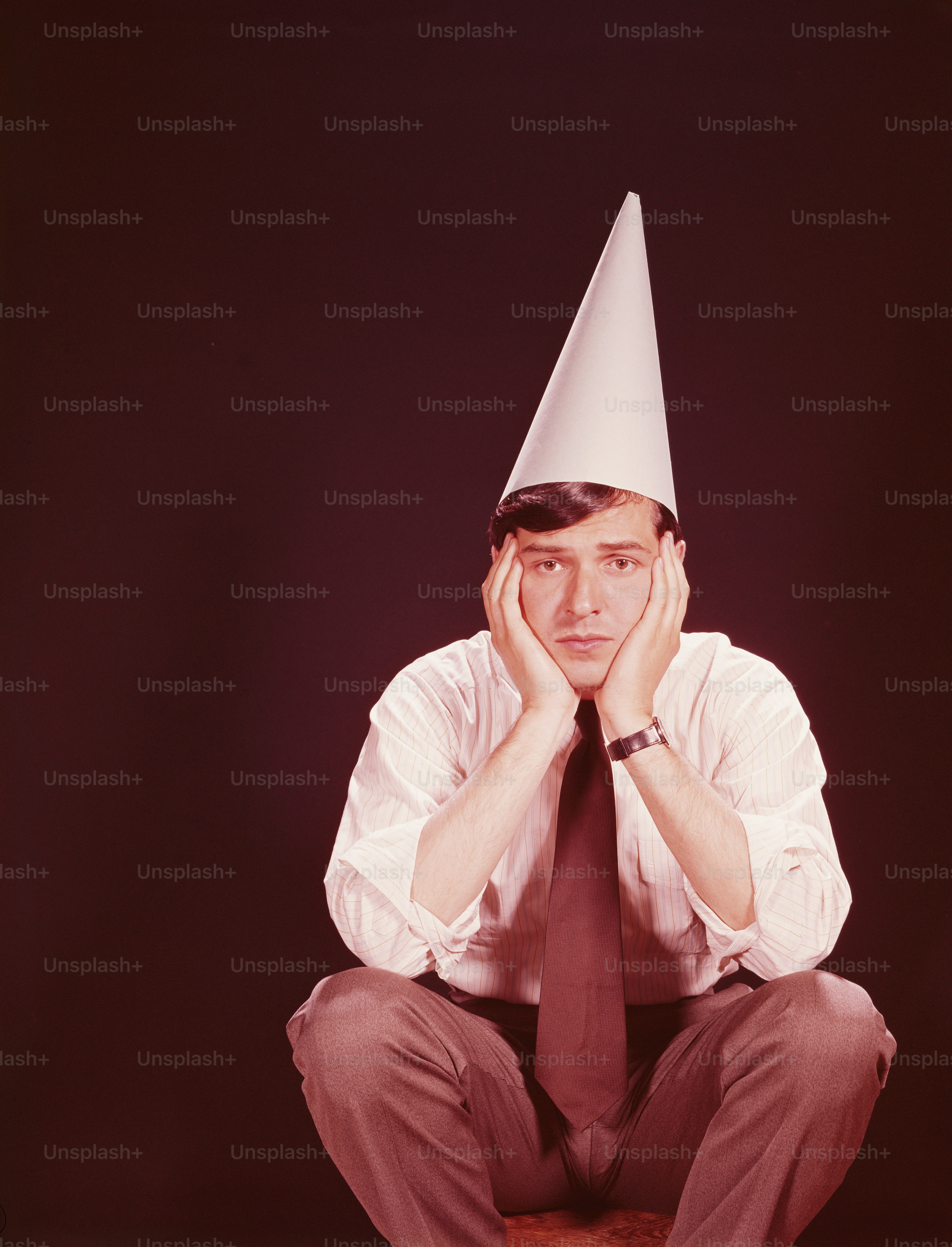 UNITED STATES - CIRCA 1970s: Man sitting on stool, wearing dunce's hat ...