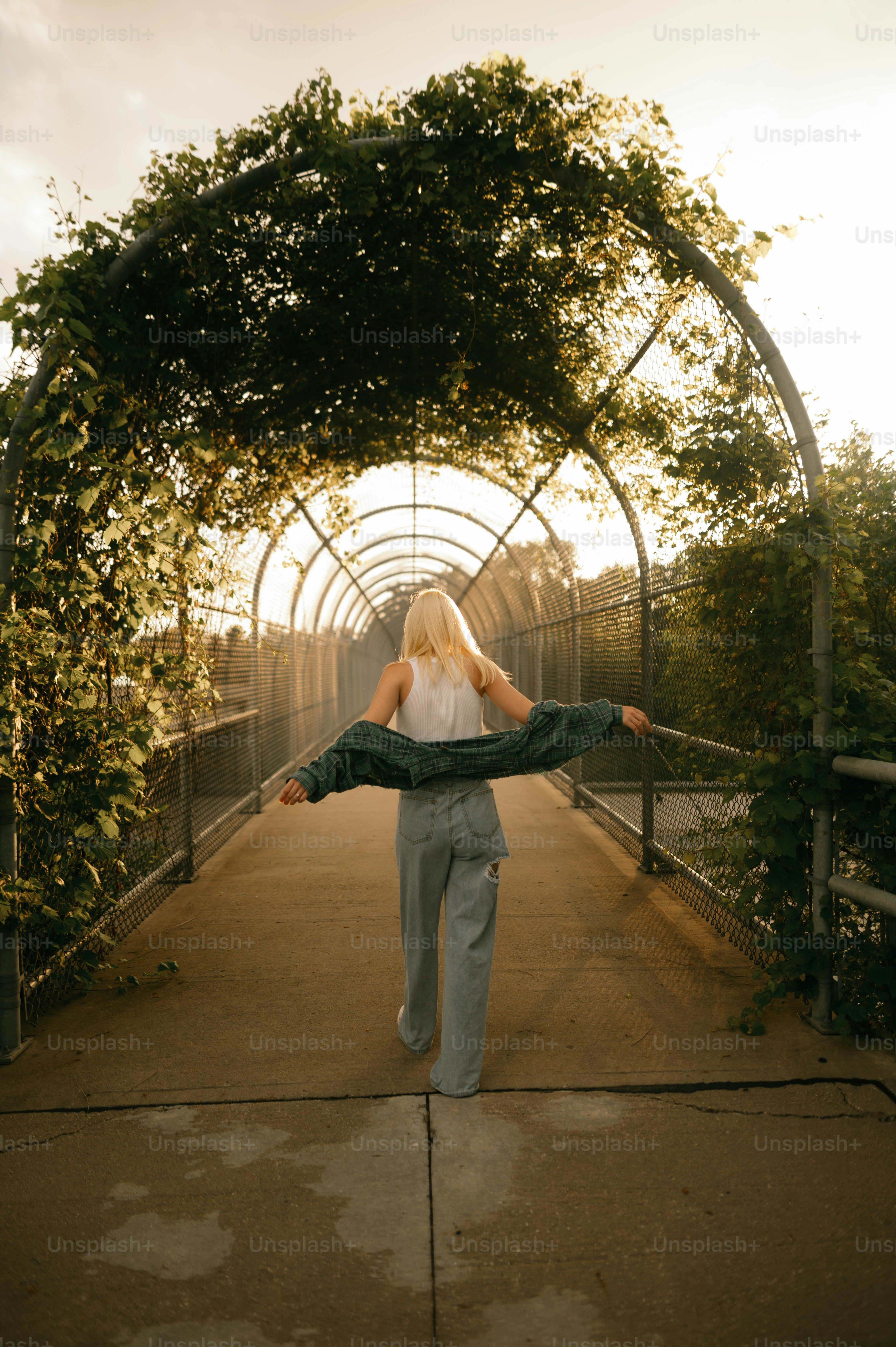 A woman walking down a walkway holding onto a jacket photo – Portrait ...