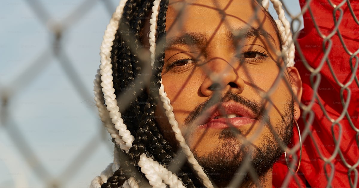 A Man With Dreadlocks Standing Behind A Chain Link Fence Photo
