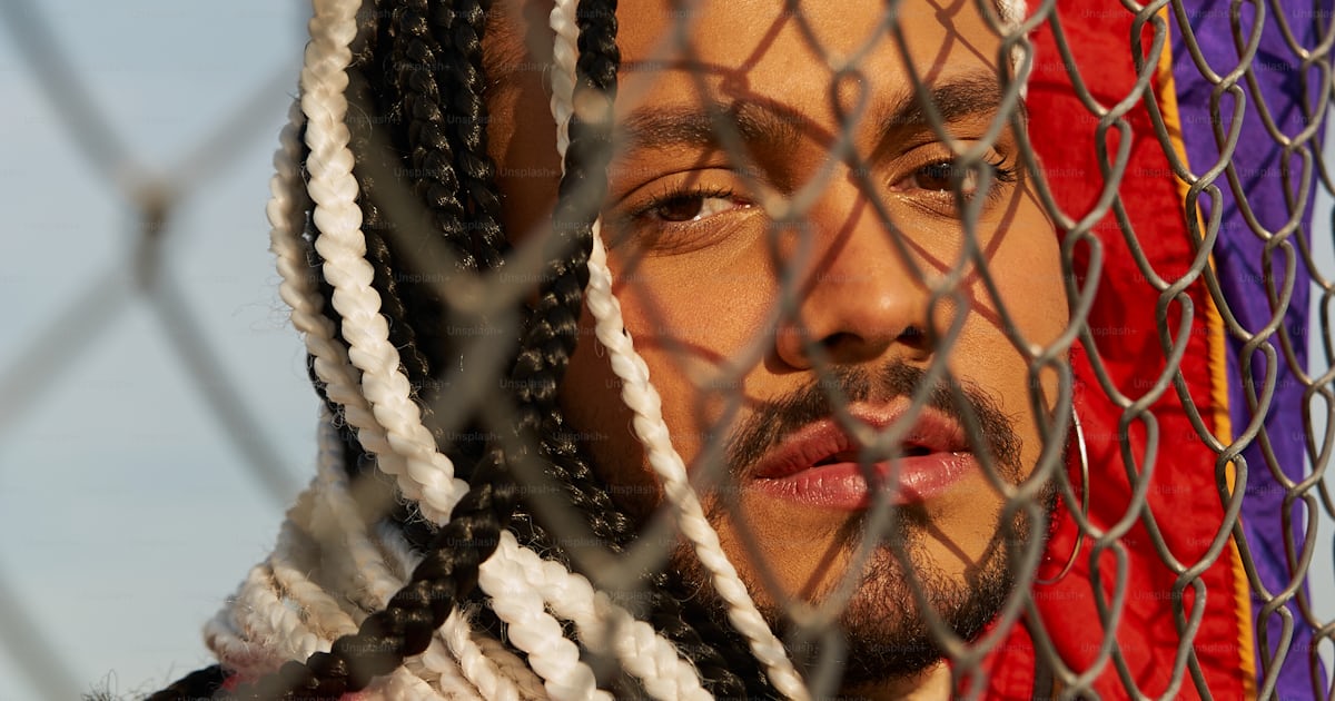 A Man With Dreadlocks Standing Behind A Chain Link Fence Photo Fence