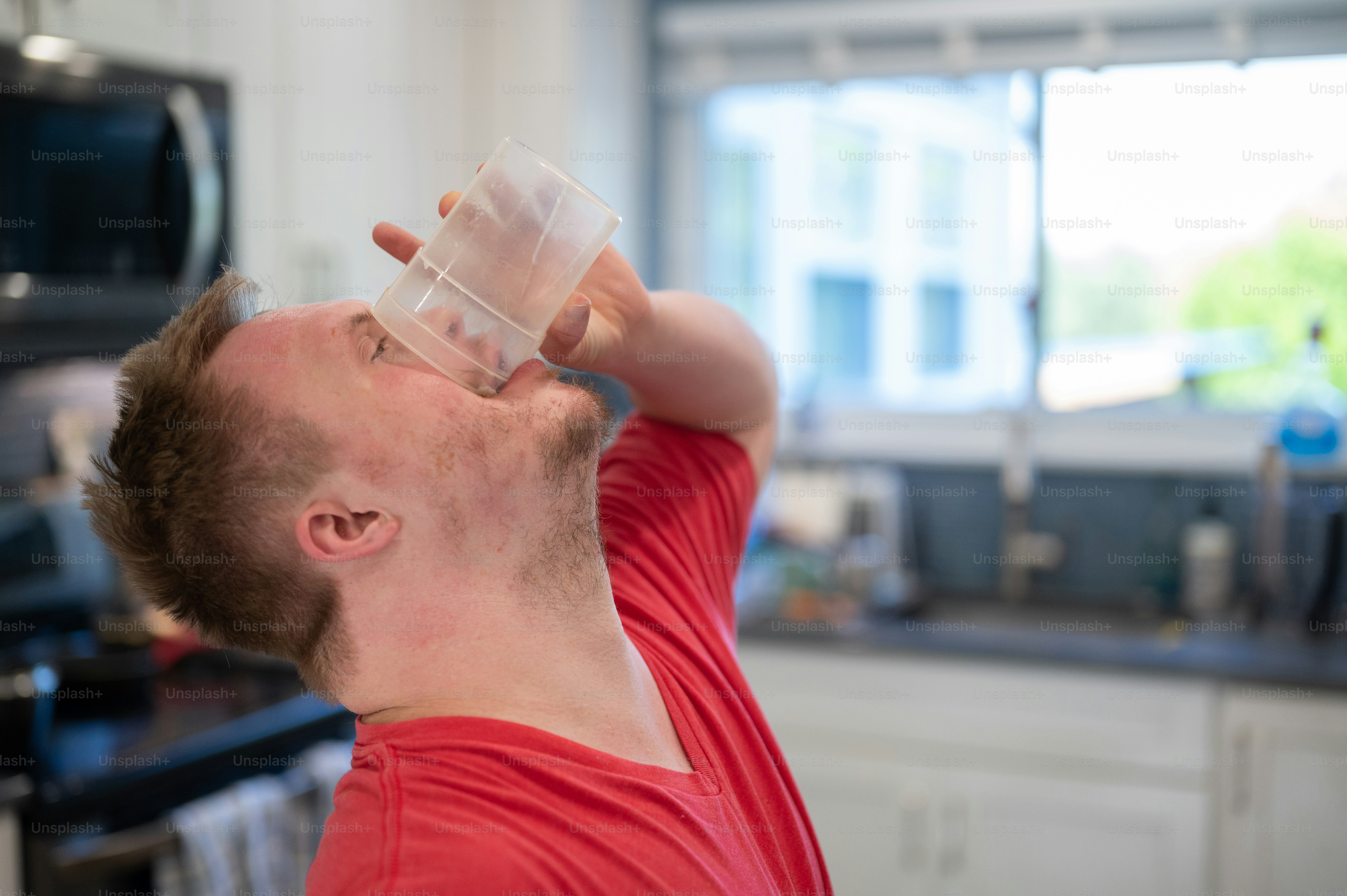A man drinking from a plastic cup in a kitchen photo – Drink Image on ...
