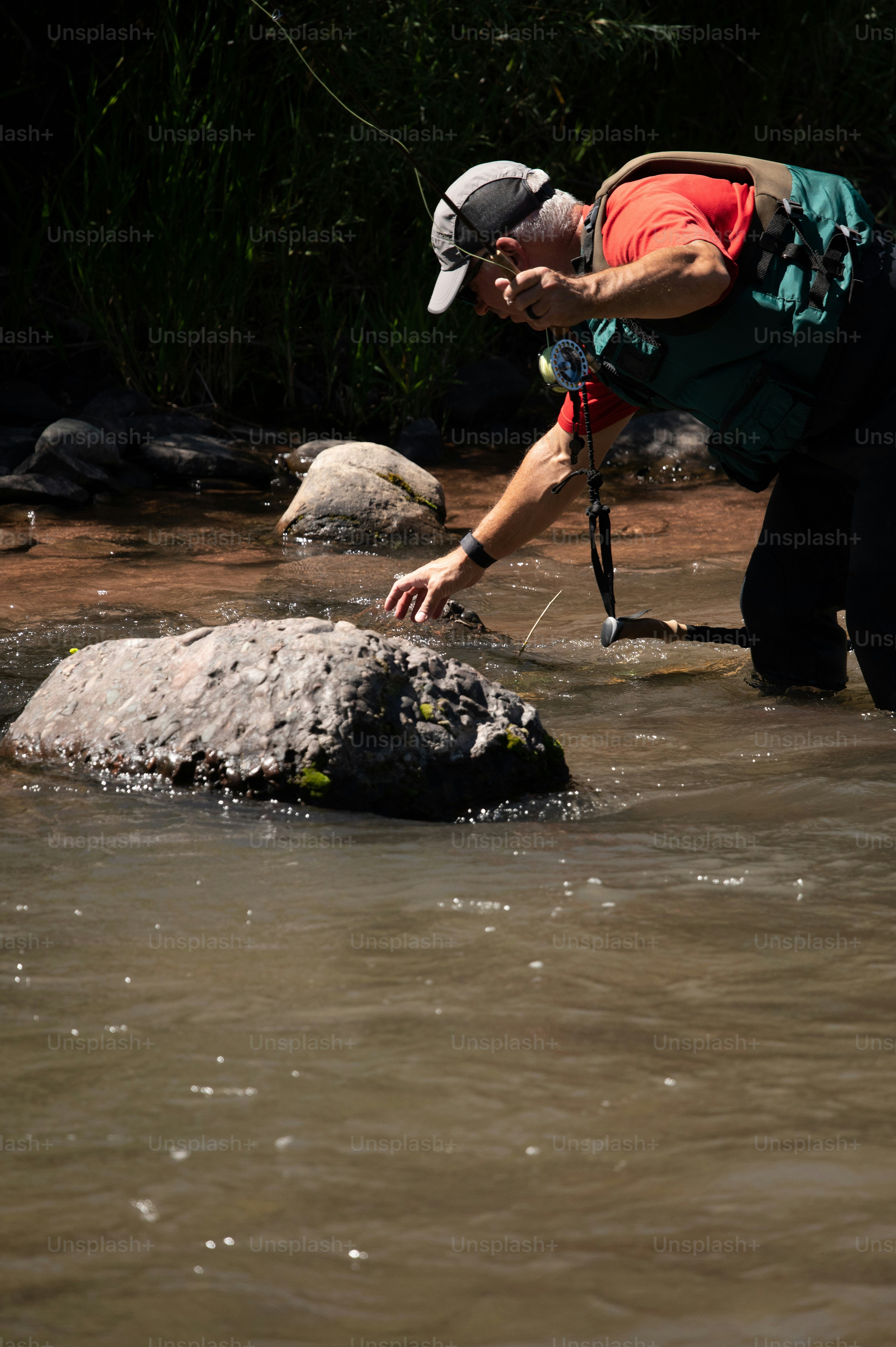 Foto Un hombre parado sobre una roca en un río – Pescar Imagen en Unsplash