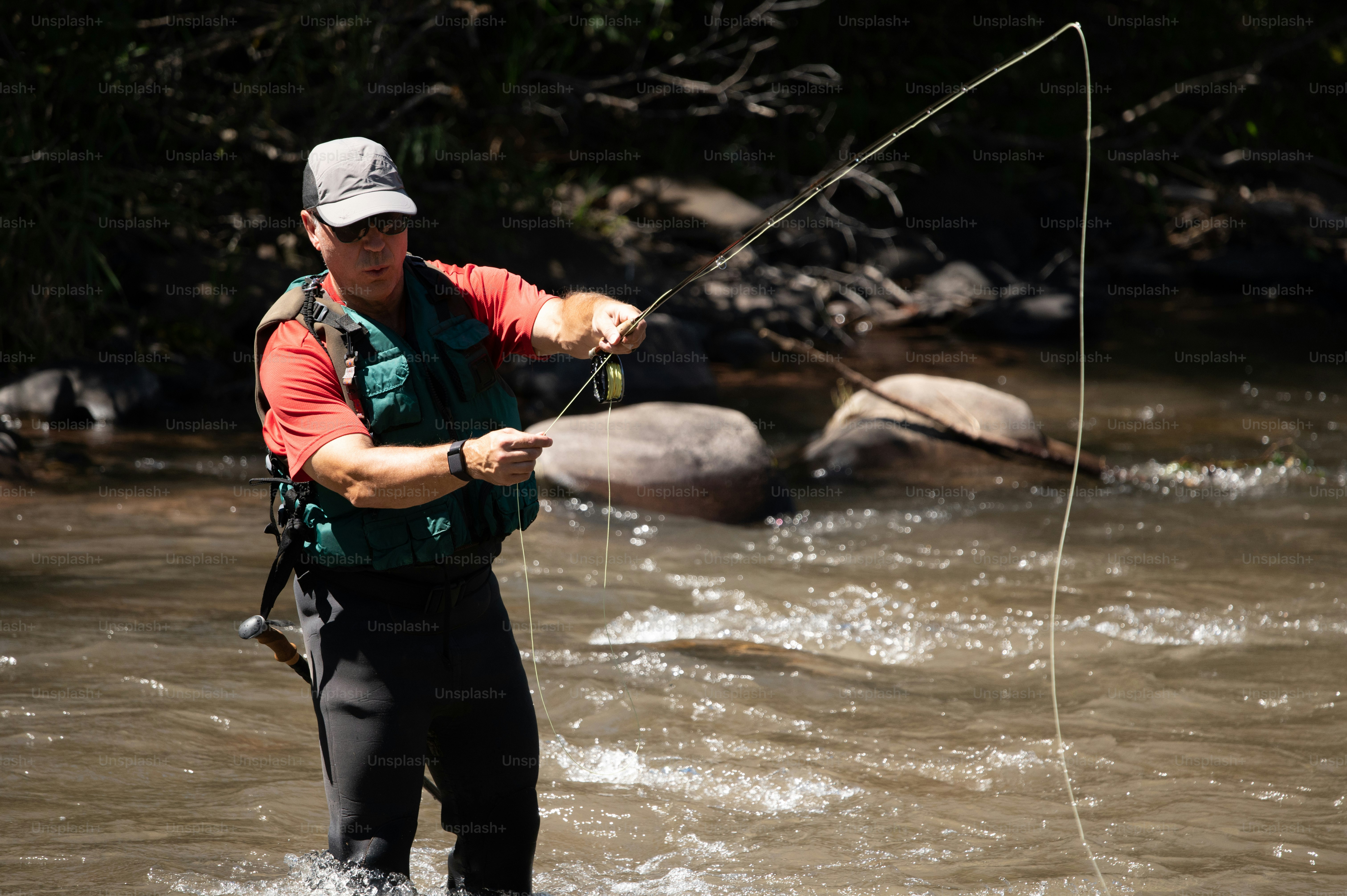 A man standing in a river holding a fishing rod photo – River Image on ...