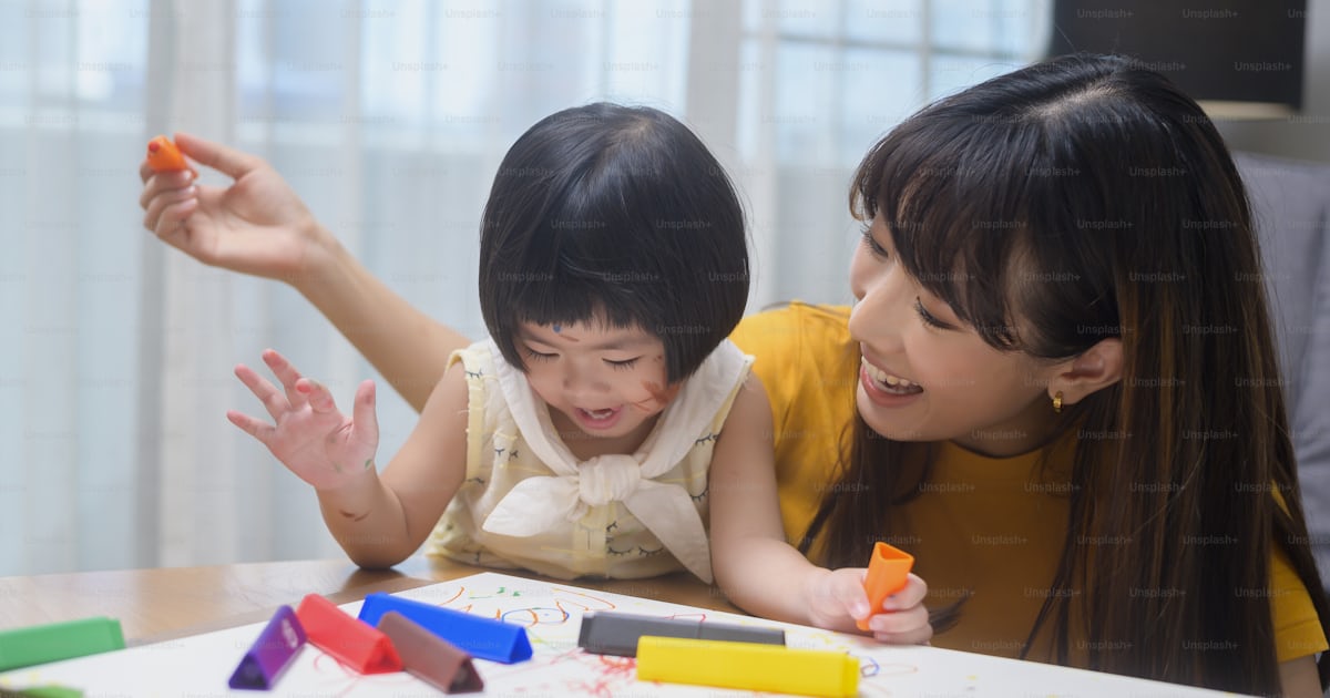Une Jeune Maman Aidant Sa Fille à Dessiner Avec Des Crayons De Couleur