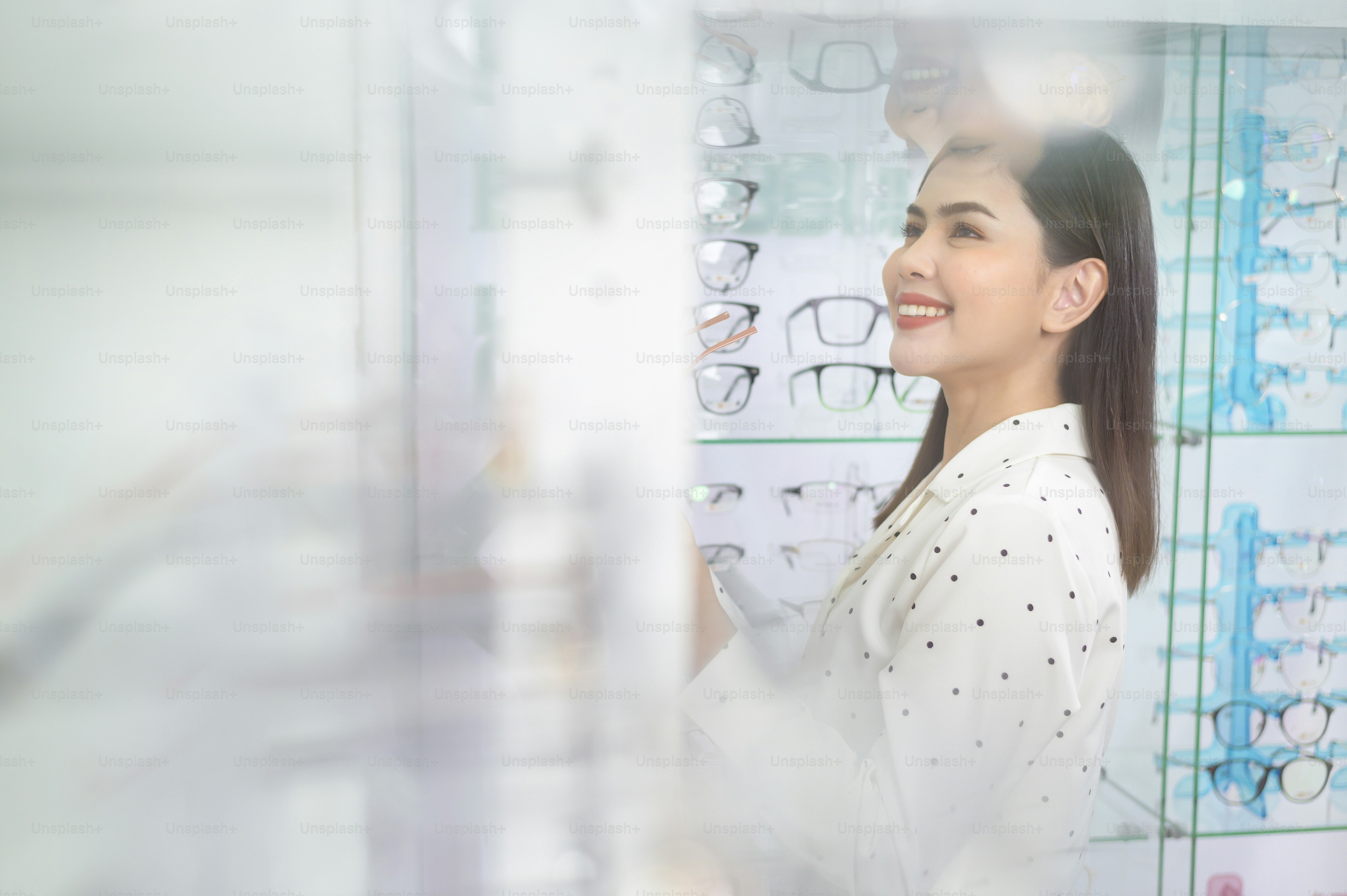 A young female customer choosing glasses in optical center, Eyecare ...
