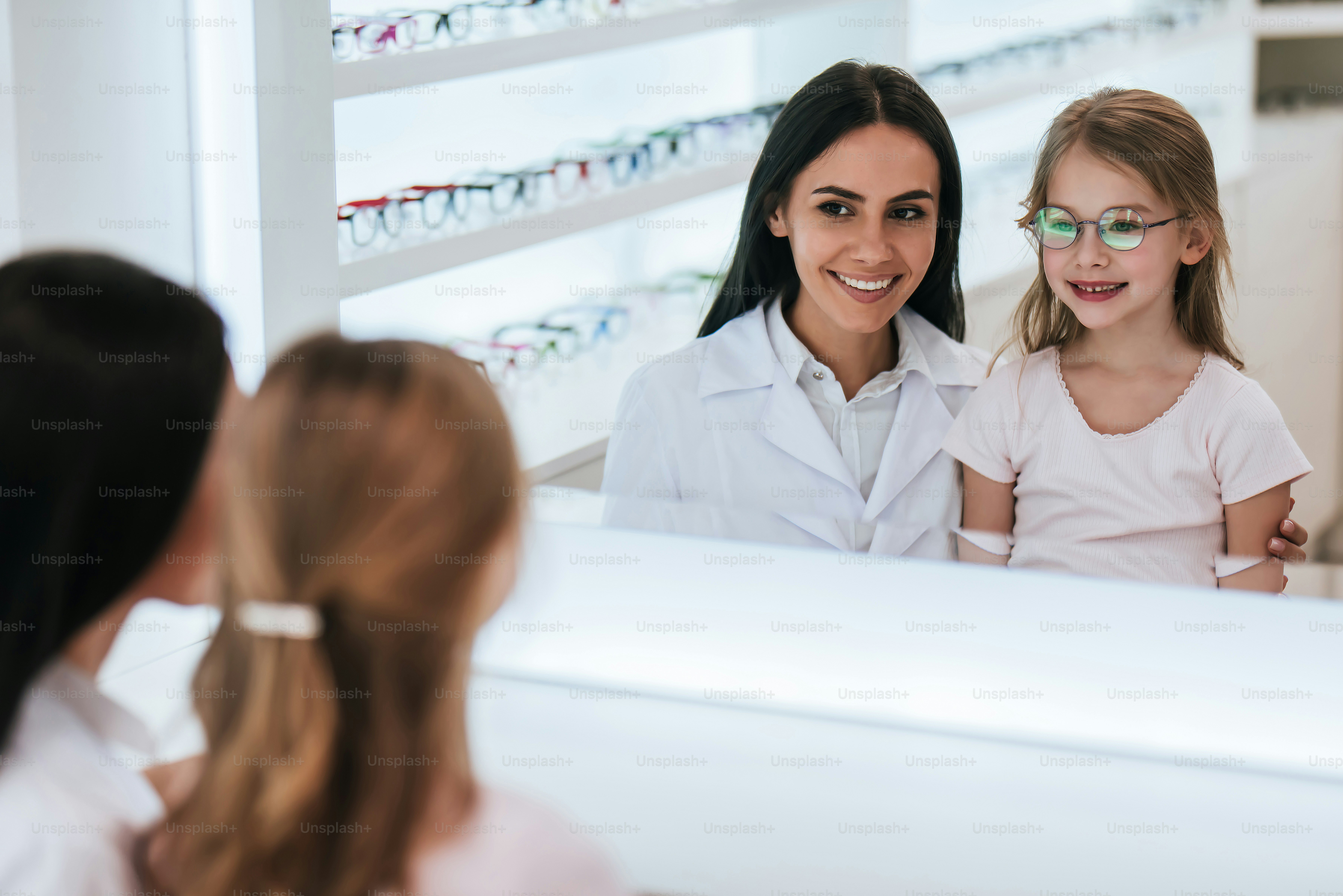 Attractive female doctor ophthalmologist is helping little cute girl to ...