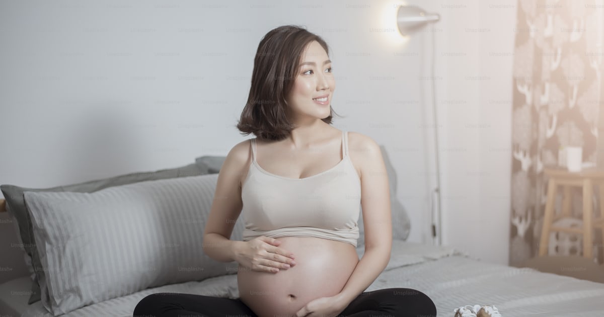 아름 다운 아시아 임신 한 여자는 침대에 앉아 그녀의 배를 만지고 사진 Unsplash의 임신한 이미지