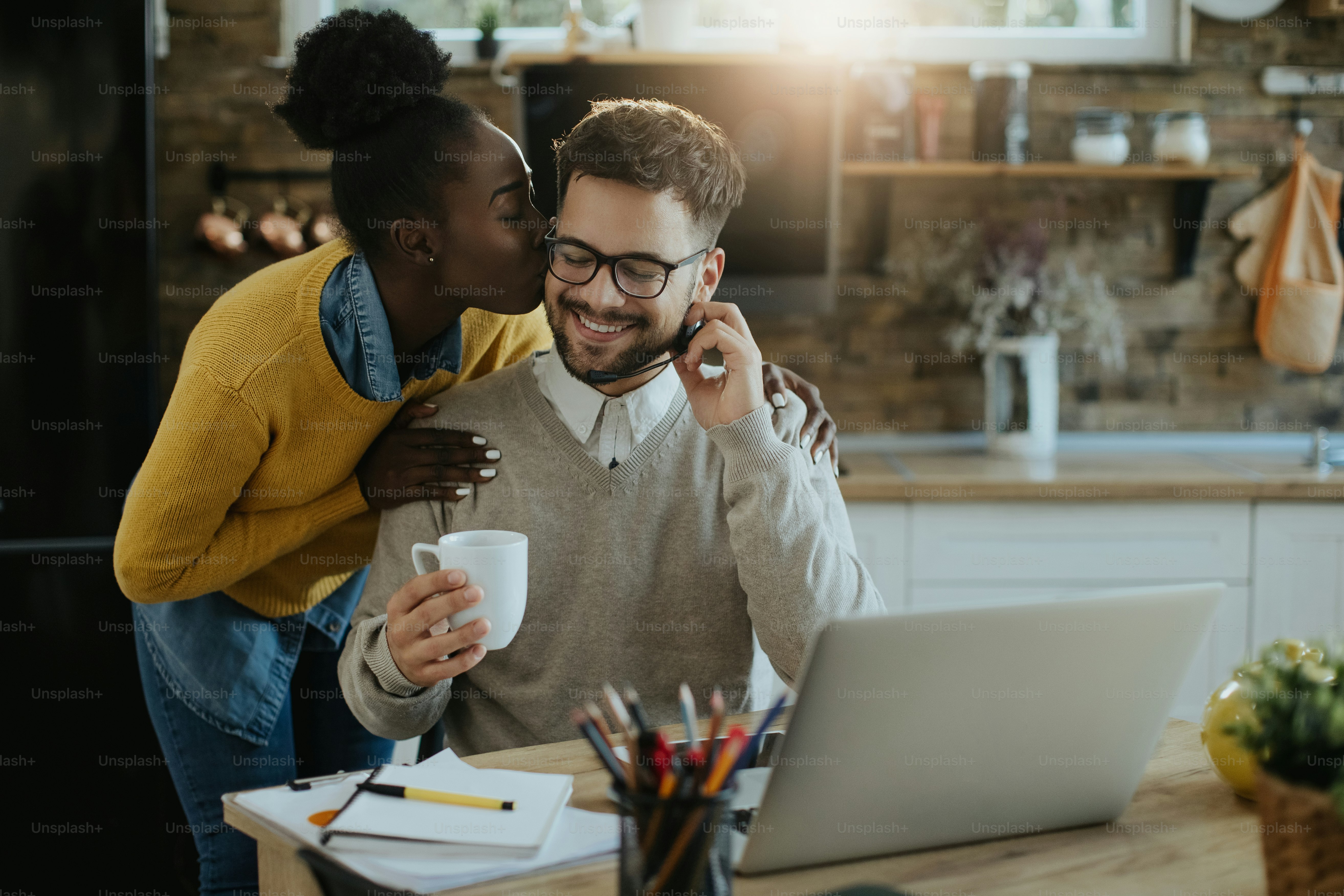 Supportive black woman kissing her husband while he is working on a ...