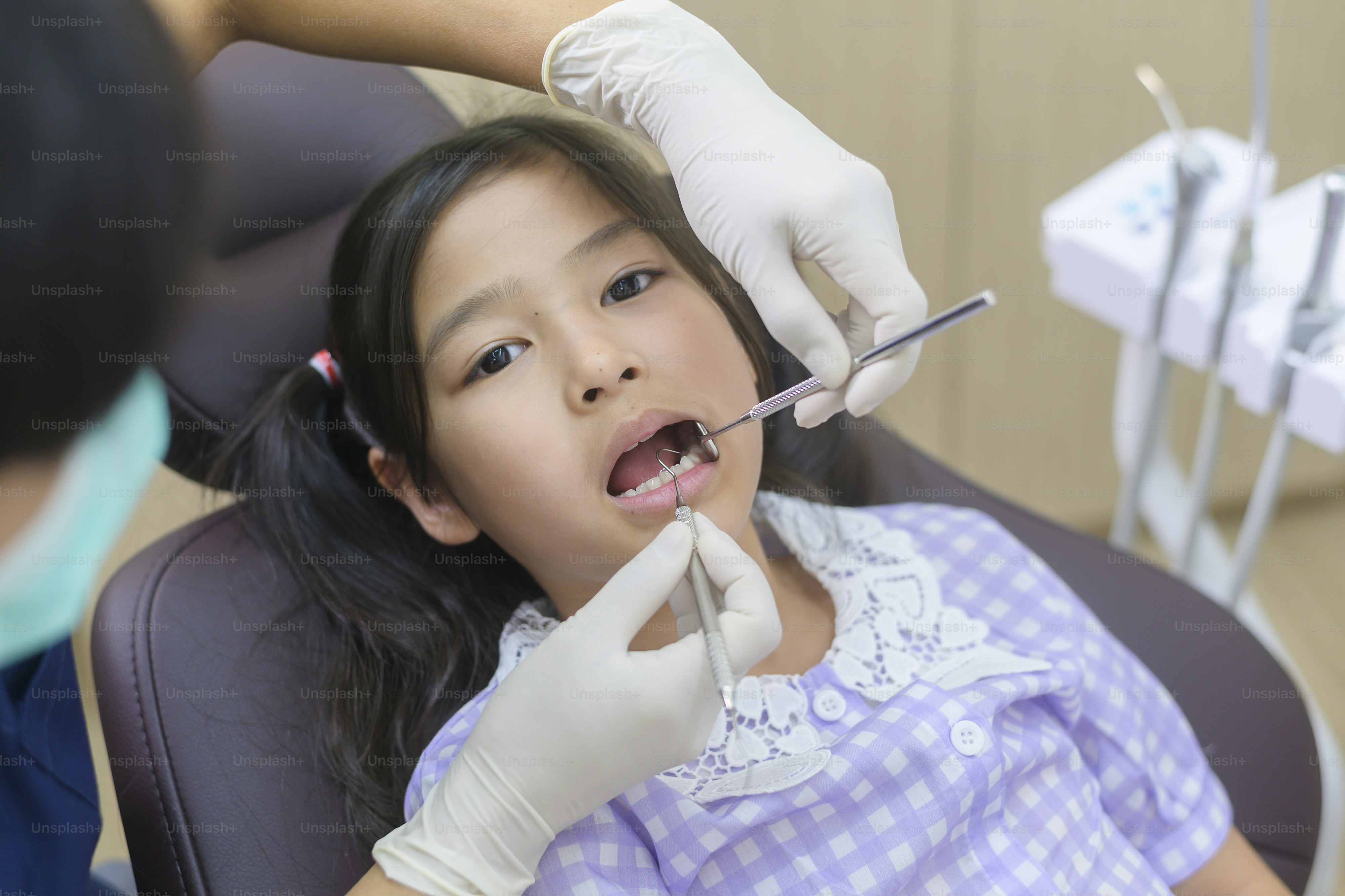 A little cute girl having teeth examined by dentist in dental clinic ...