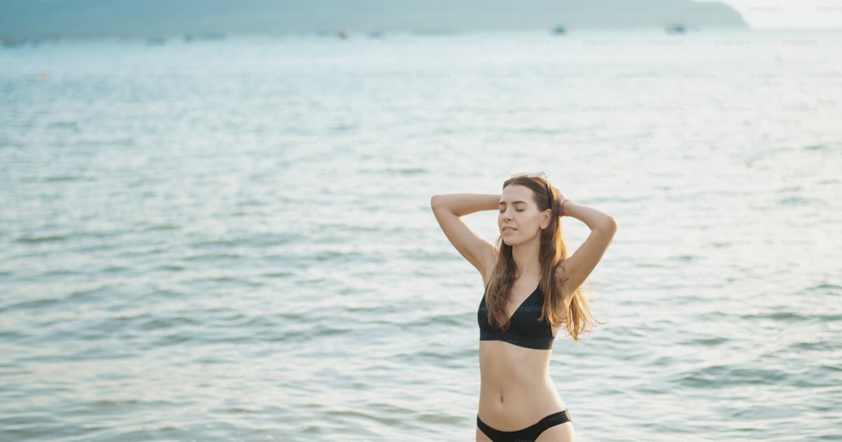검은 비키니를 입은 아름다운 여자가 해변에서 바닷물을 즐기고 있다 사진 Unsplash의 수영복을 입은 여자 이미지