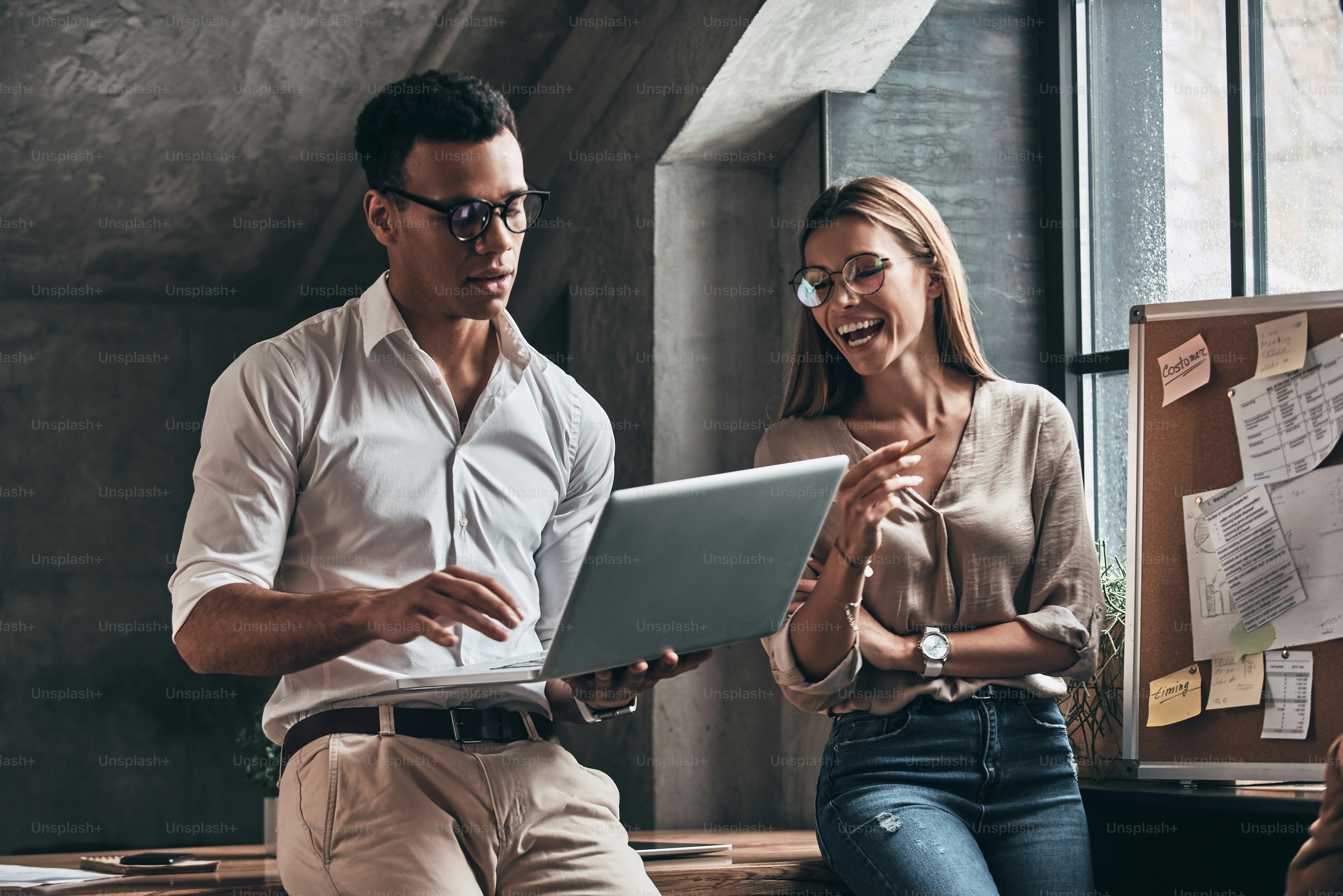 Two young business people using computer and smiling while working in ...