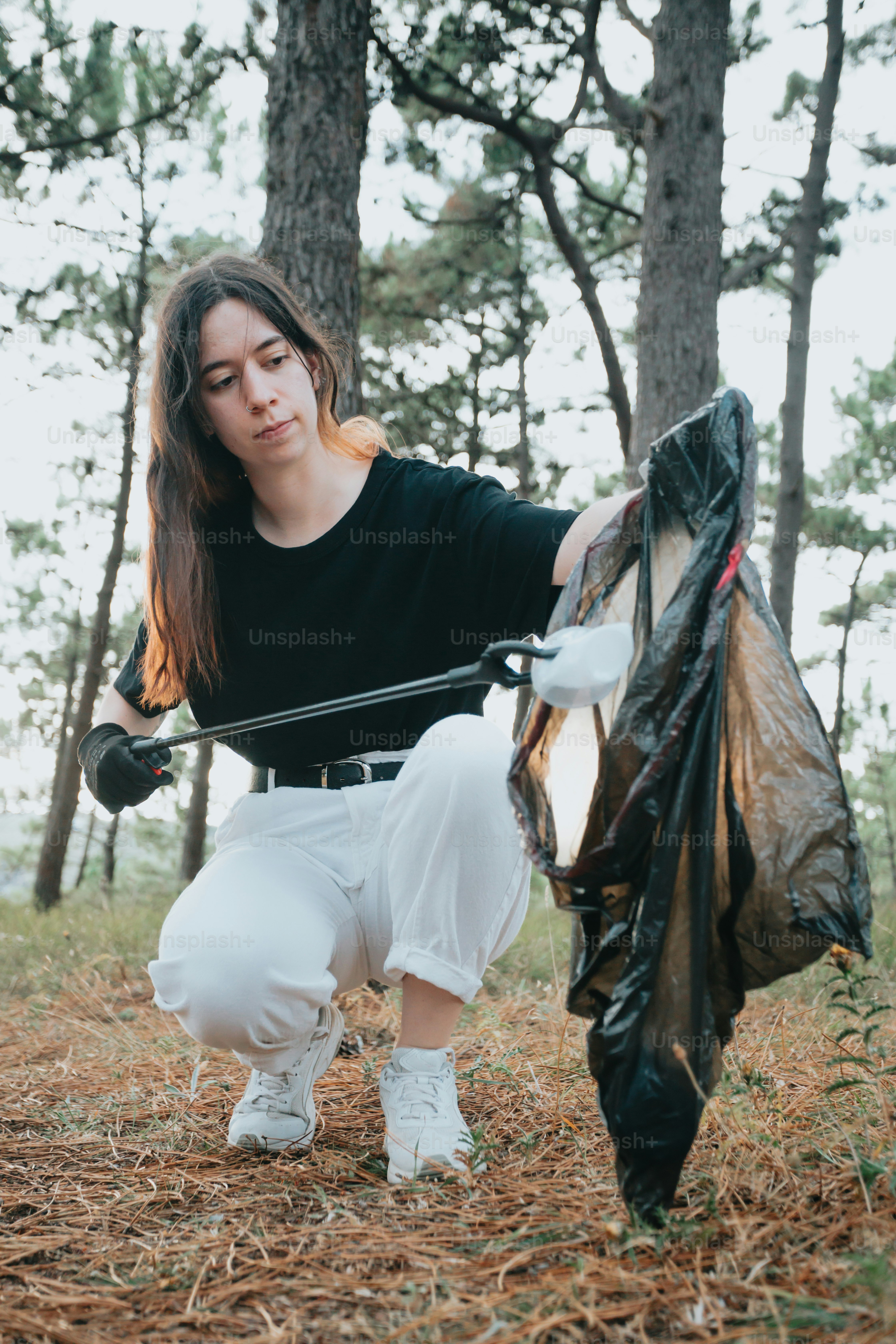 A woman holding a bag of trash in the woods photo – Litter picker Image ...