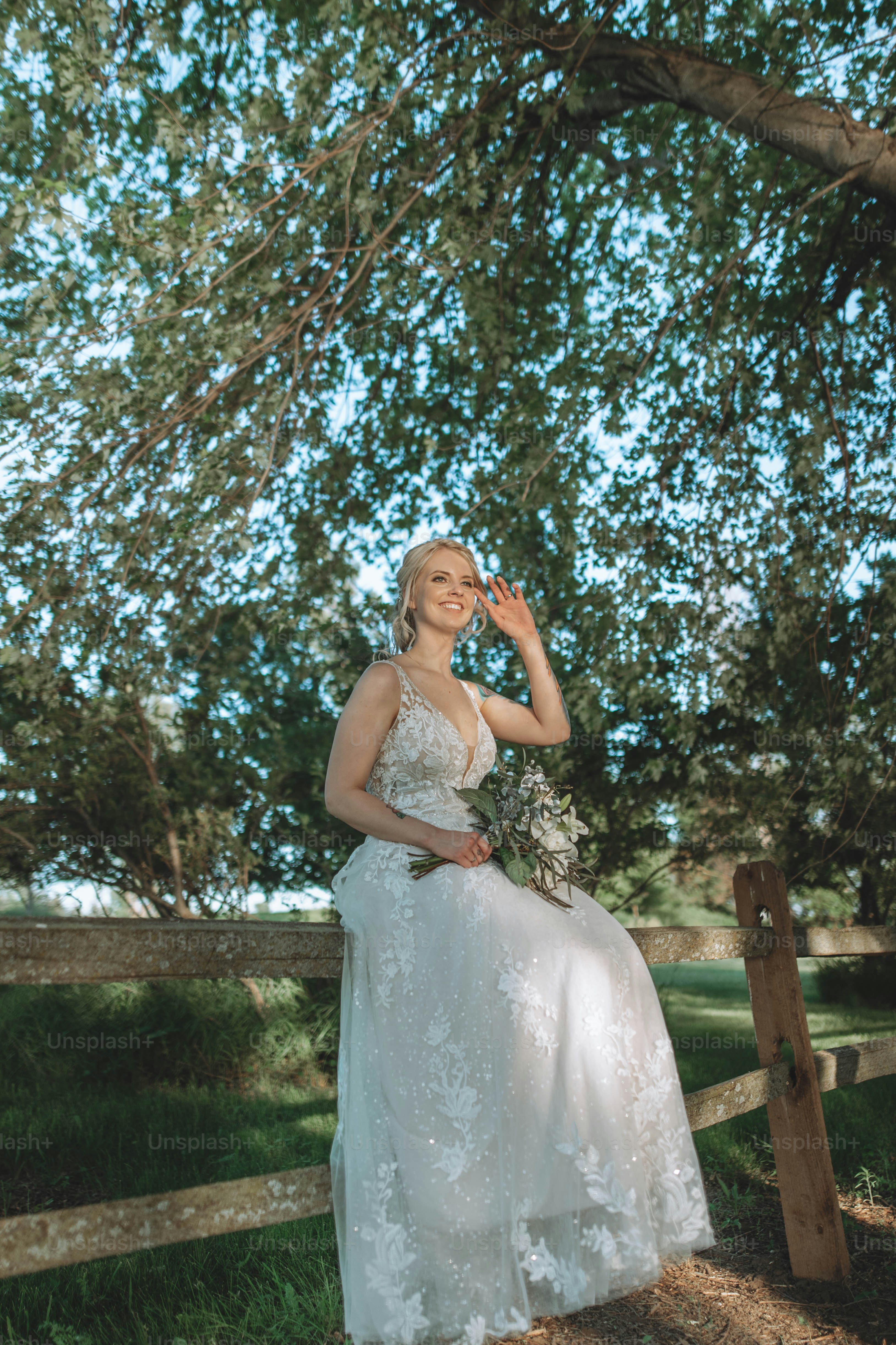 A woman in a wedding dress sitting on a fence photo – Portrait Image on ...