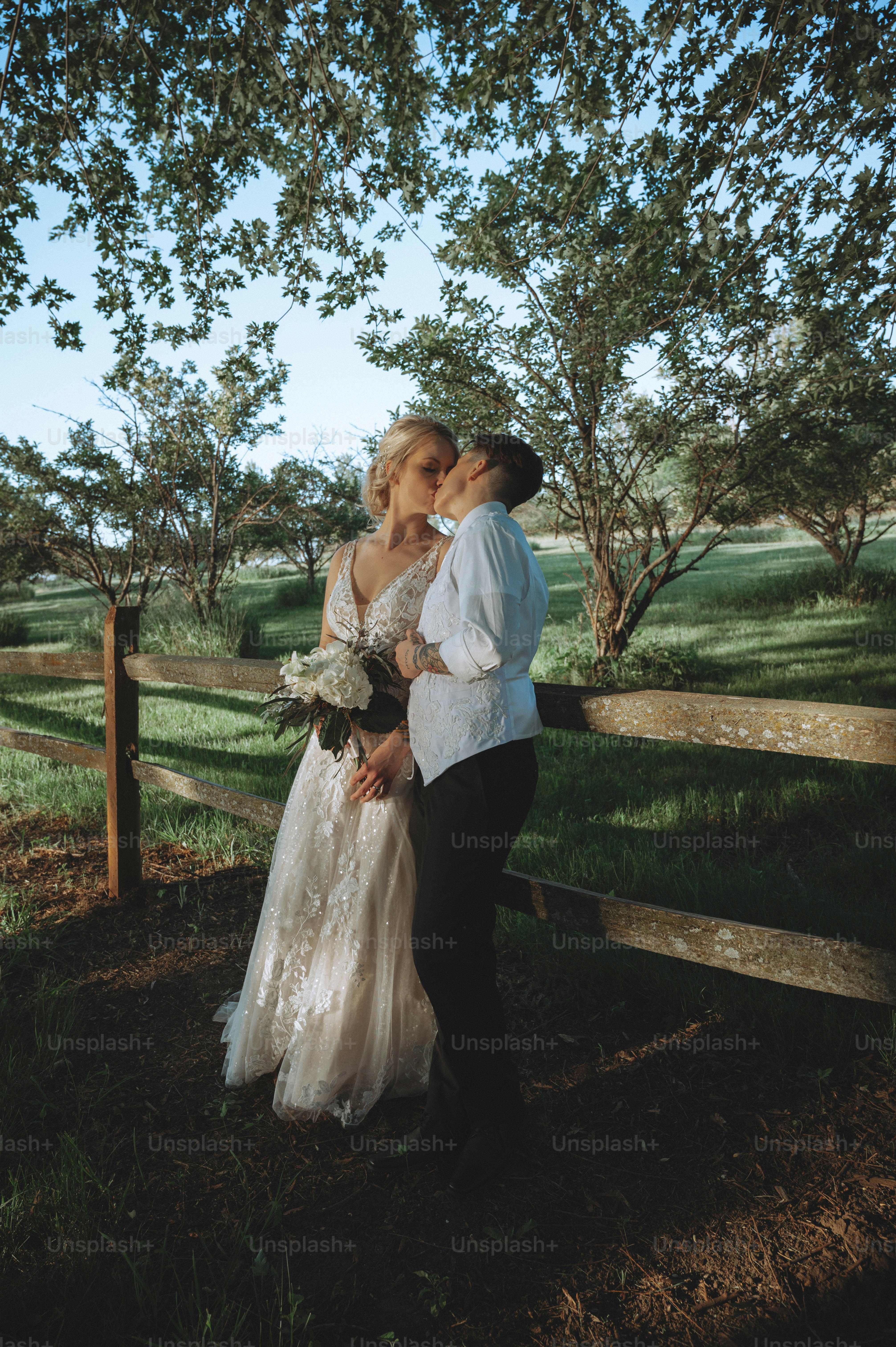 A bride and groom kissing in front of a fence photo – Wedding Image on ...