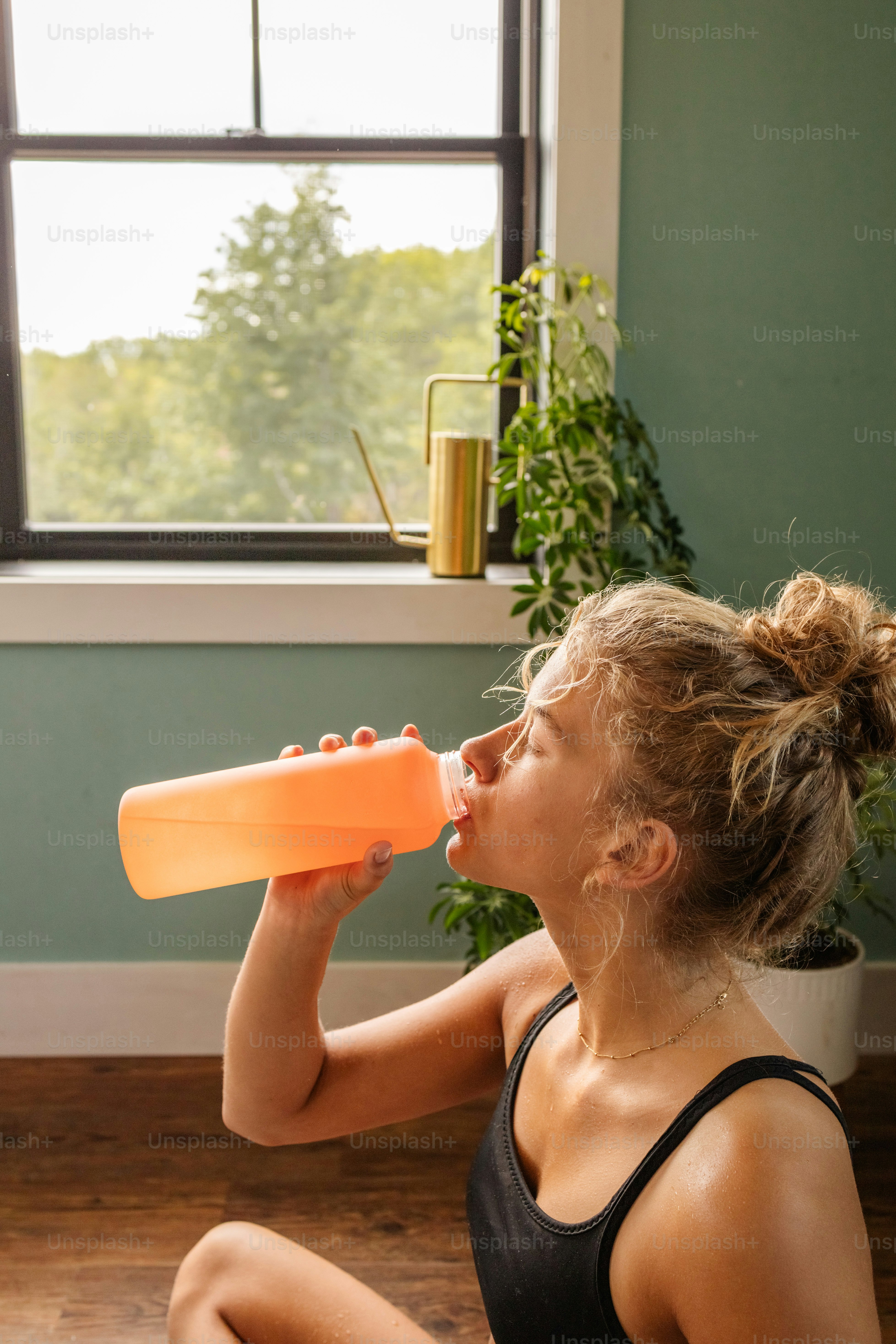 A woman sitting on the floor drinking from a bottle photo – Hydration ...