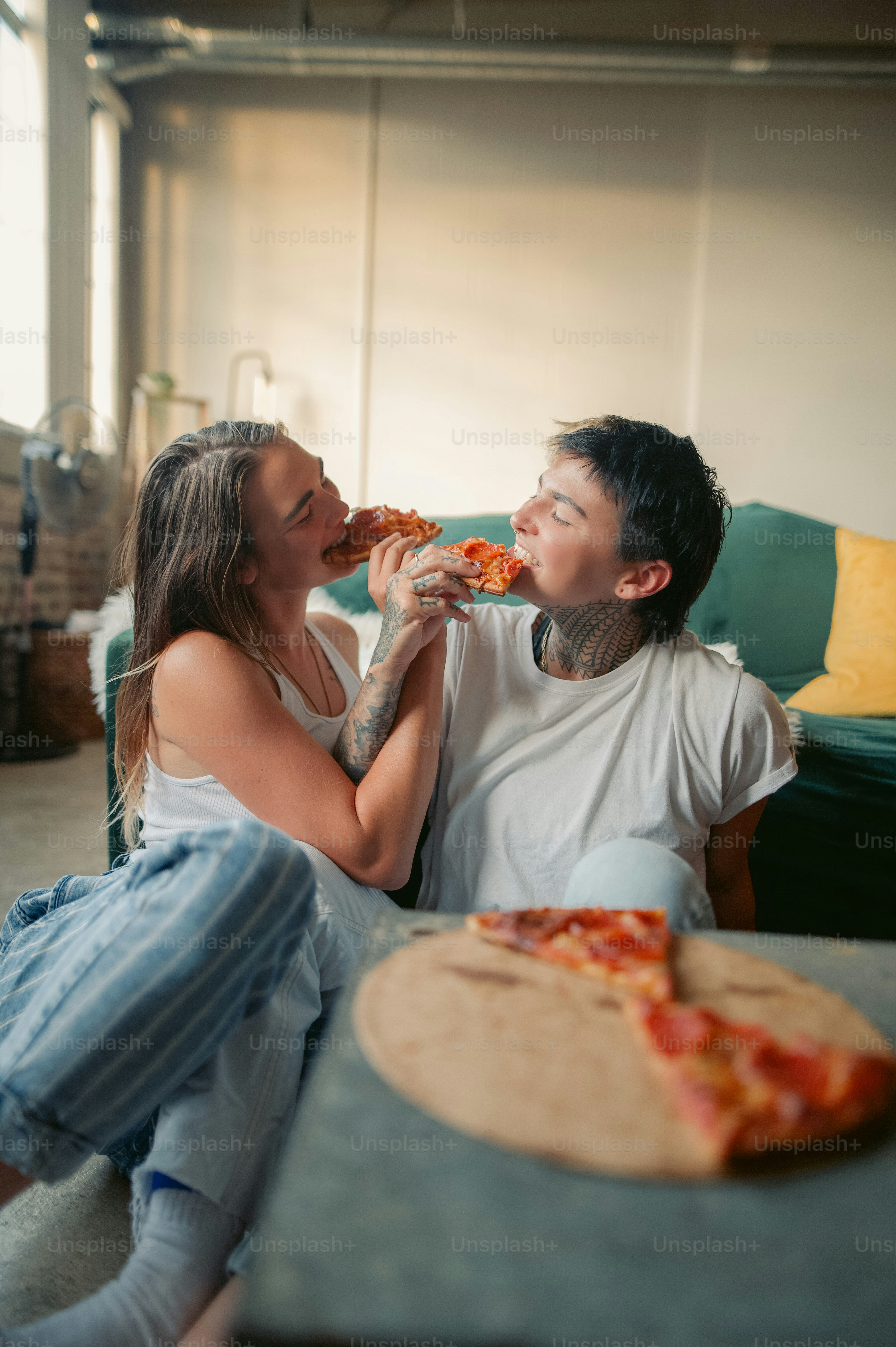 A man and a woman sitting on a couch eating pizza photo – Lgbtq Image ...