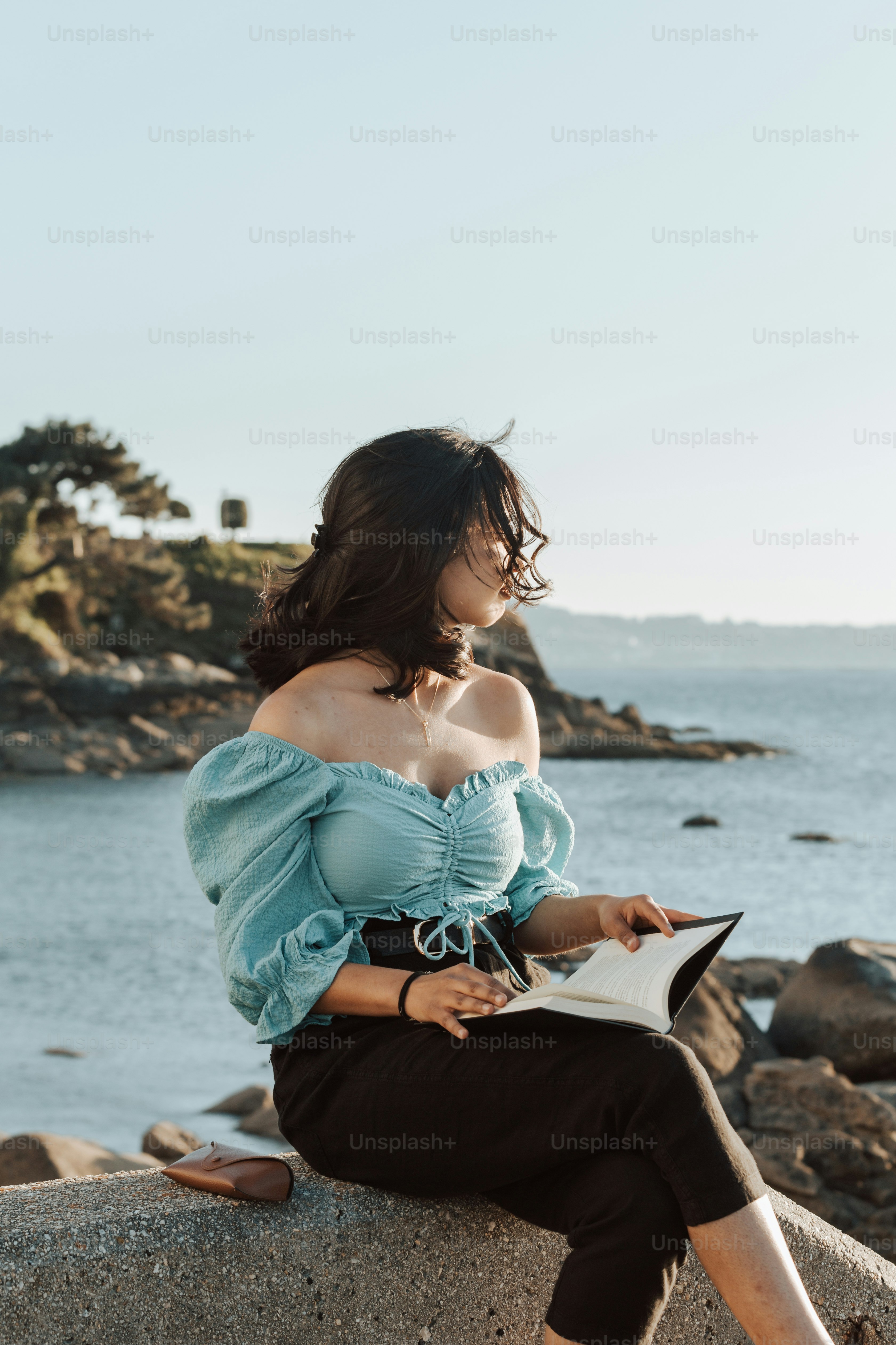 A woman sitting on a rock reading a book photo – Woman Image on Unsplash