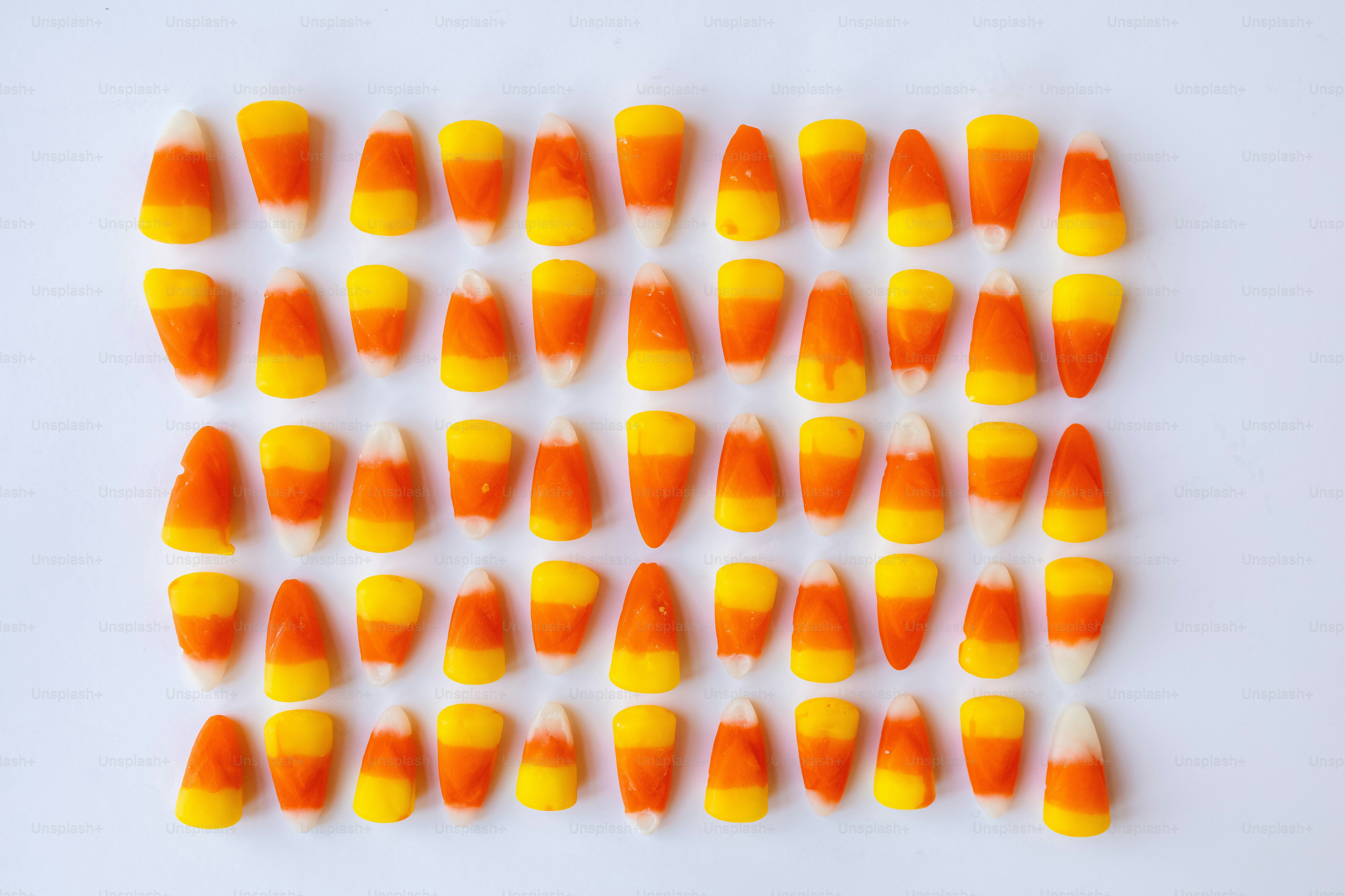 A group of orange and white candy corn on a white surface photo ...