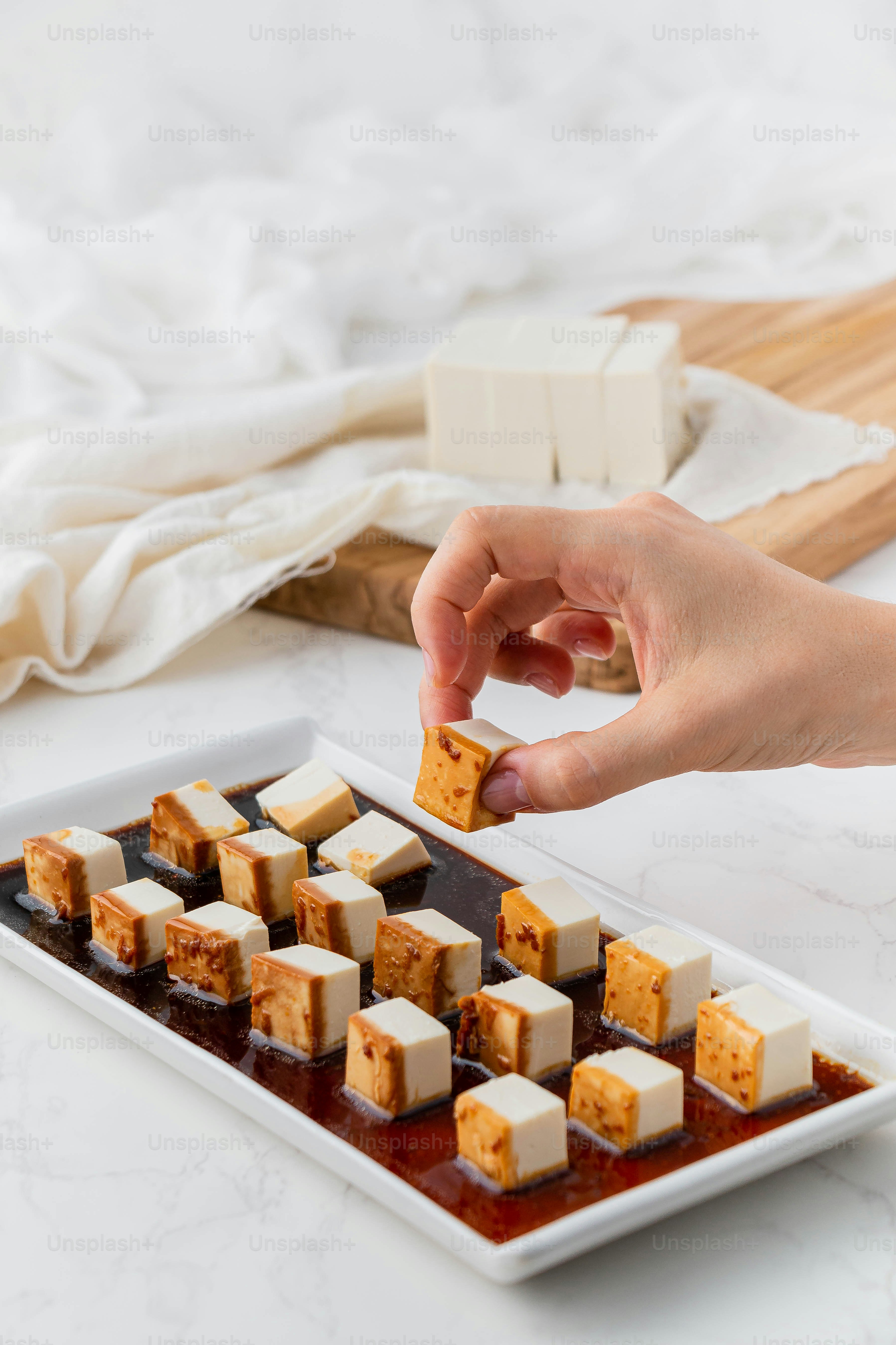 A person holding a piece of tofu over a plate of tofu photo – Clean ...