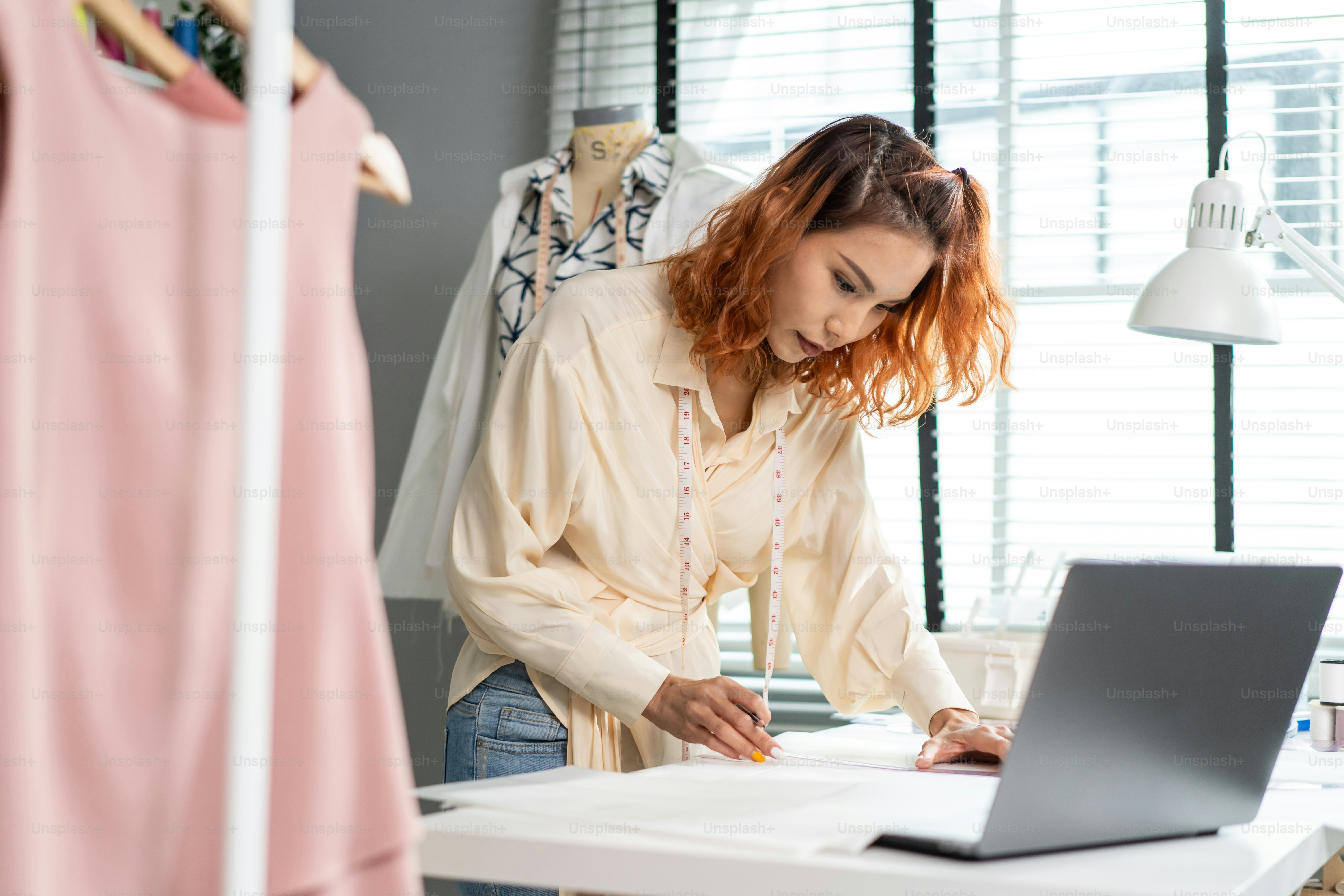 Asiatische schöne Schneiderin, die im Schneideratelier an Kleidung ...