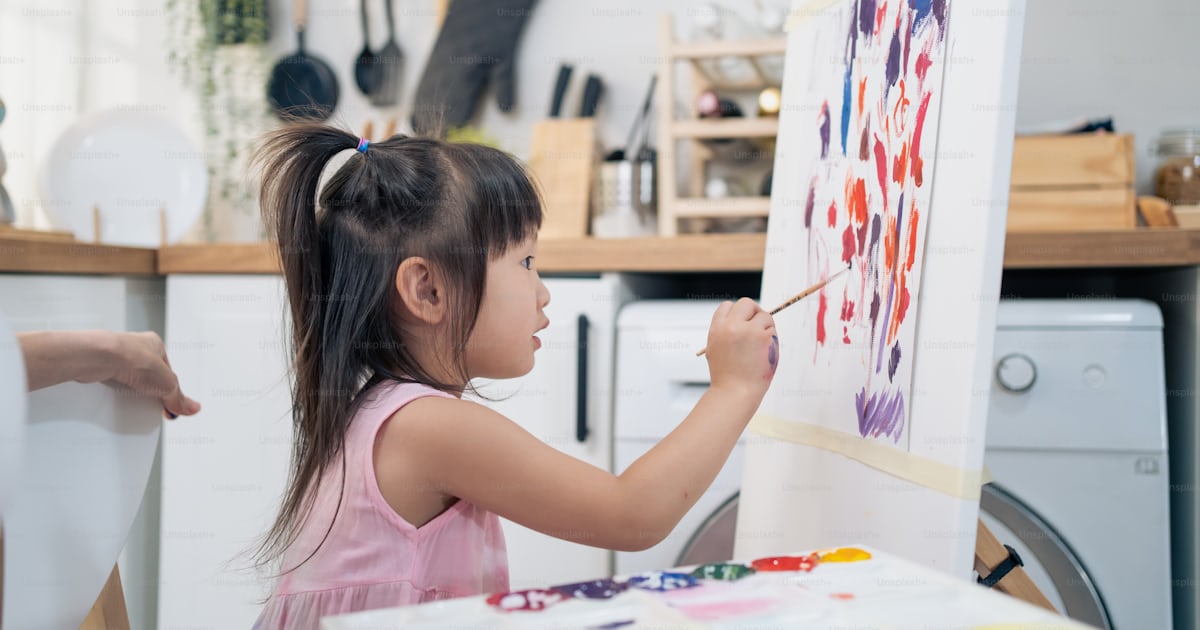 아시아의 젊은 행복한 아이 소녀가 거실에서 그림 보드에 색칠하고 있다 작고 사랑스러운 아이는 수채화 물감으로 예술 그림을