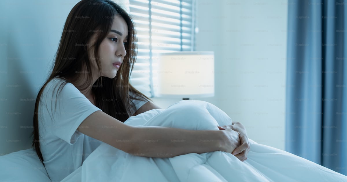 아시아의 아름다운 화가 우울한 소녀가 침실의 침대에 혼자 앉아 있습니다 매력적인 불행한 젊은 여성은 삶의 문제로 외롭고 화가
