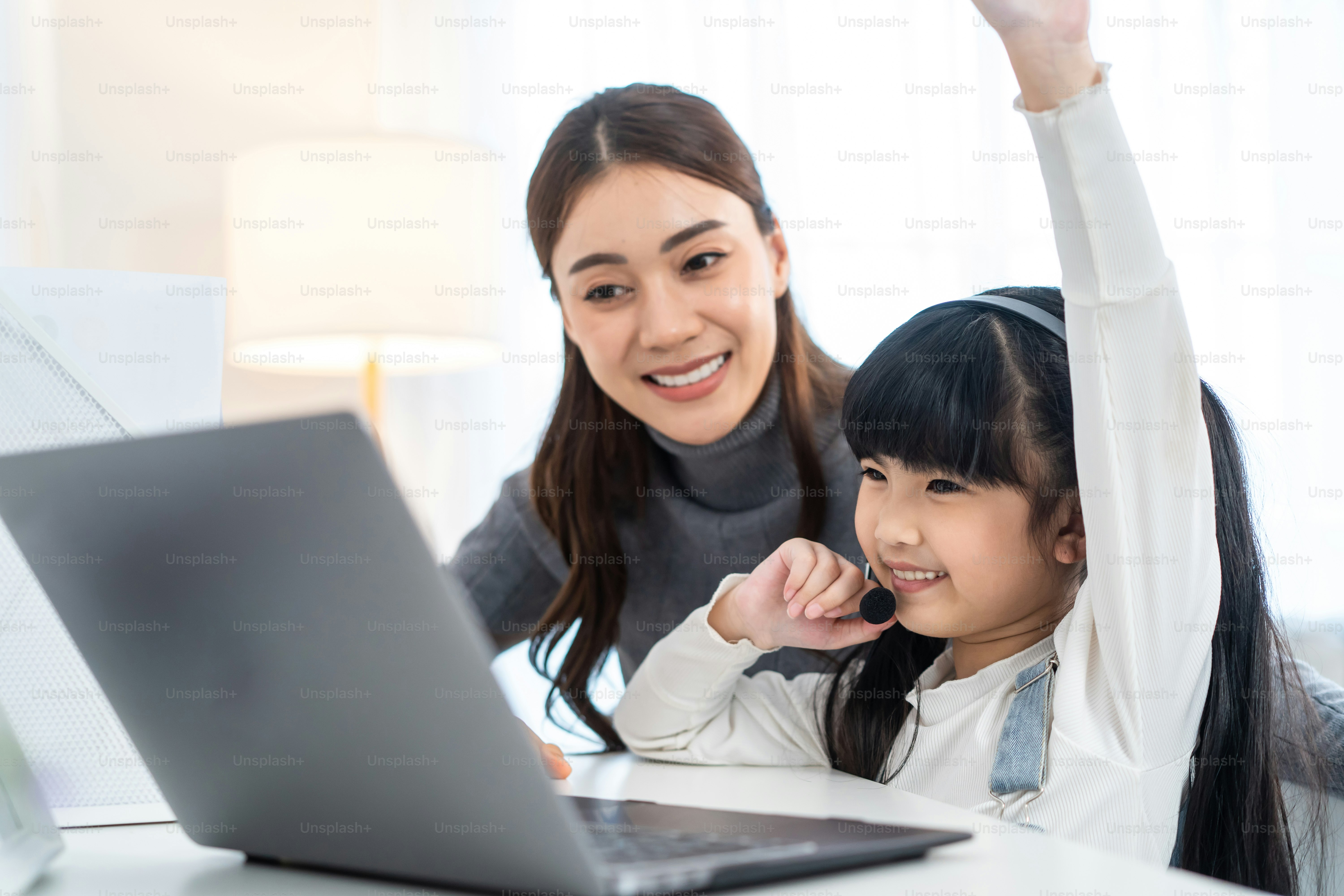 Niña asiática que aprende clase en línea en casa con su madre. El niño en edad preescolar usa ...