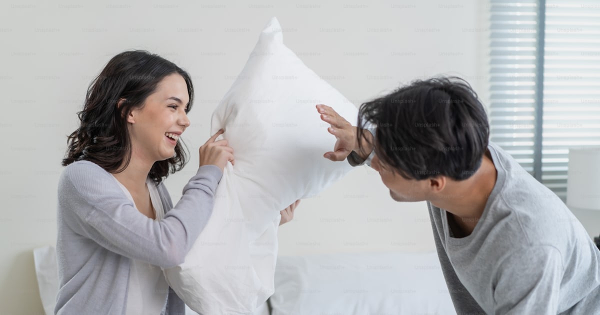 아시아의 젊은 아름다운 사랑하는 커플은 침대에서 함께 베개 싸움을 한다 매력적인 새로운 결혼 남녀는 행복을 느끼고 집안의