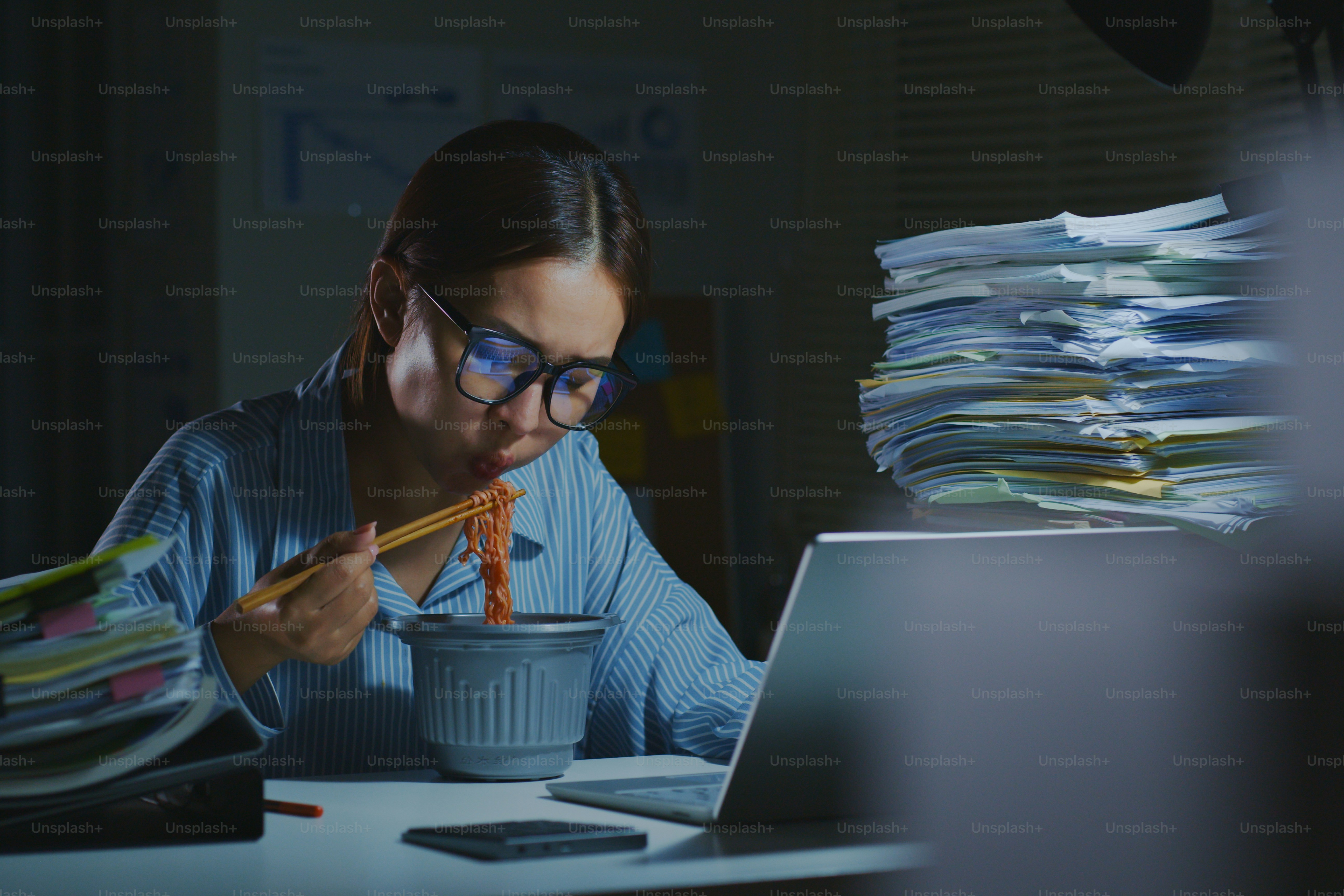 Young Asian office employee eating instant noodles while working on ...
