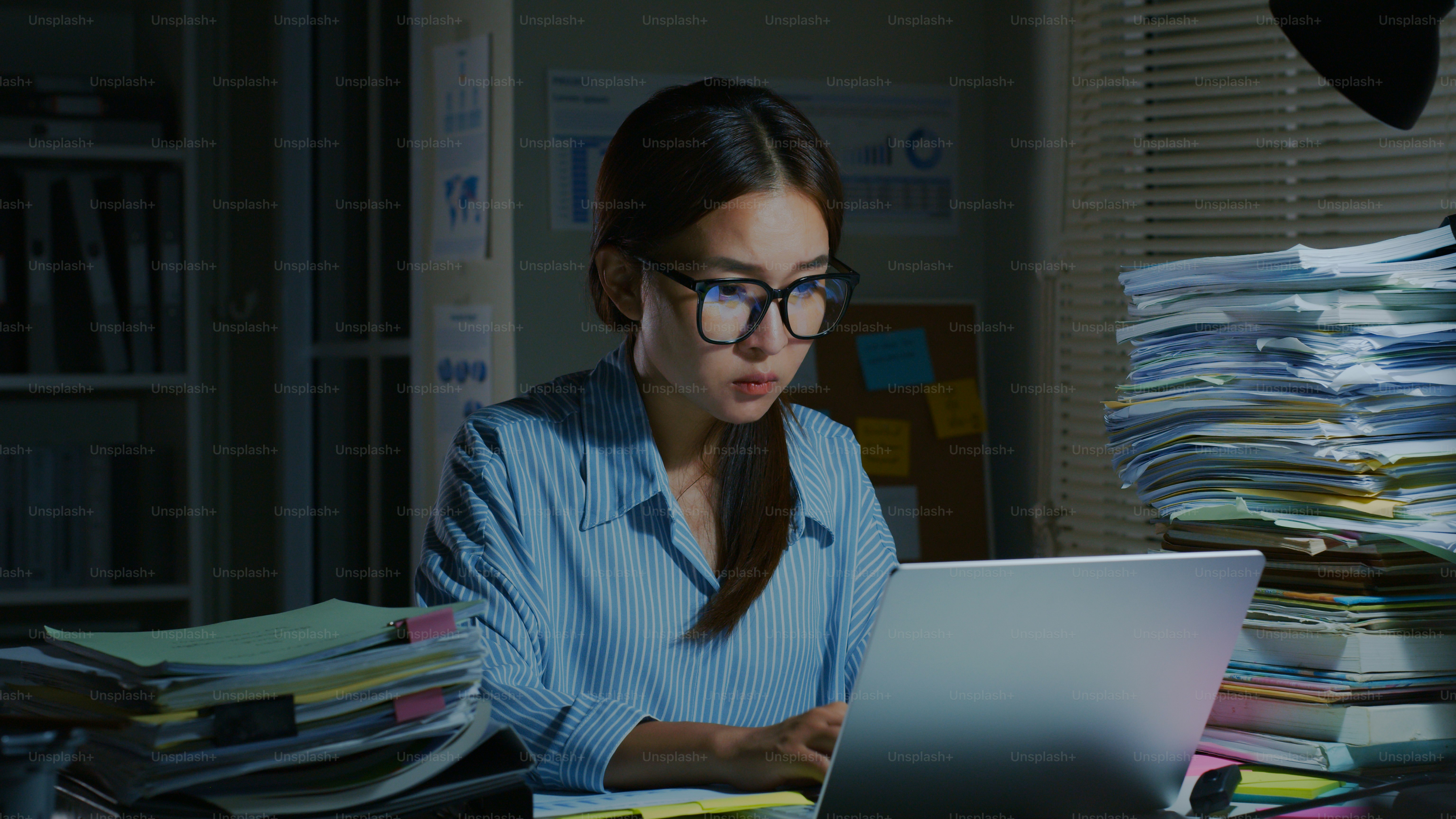 Overworked Asian office employee using laptop computer for working late ...
