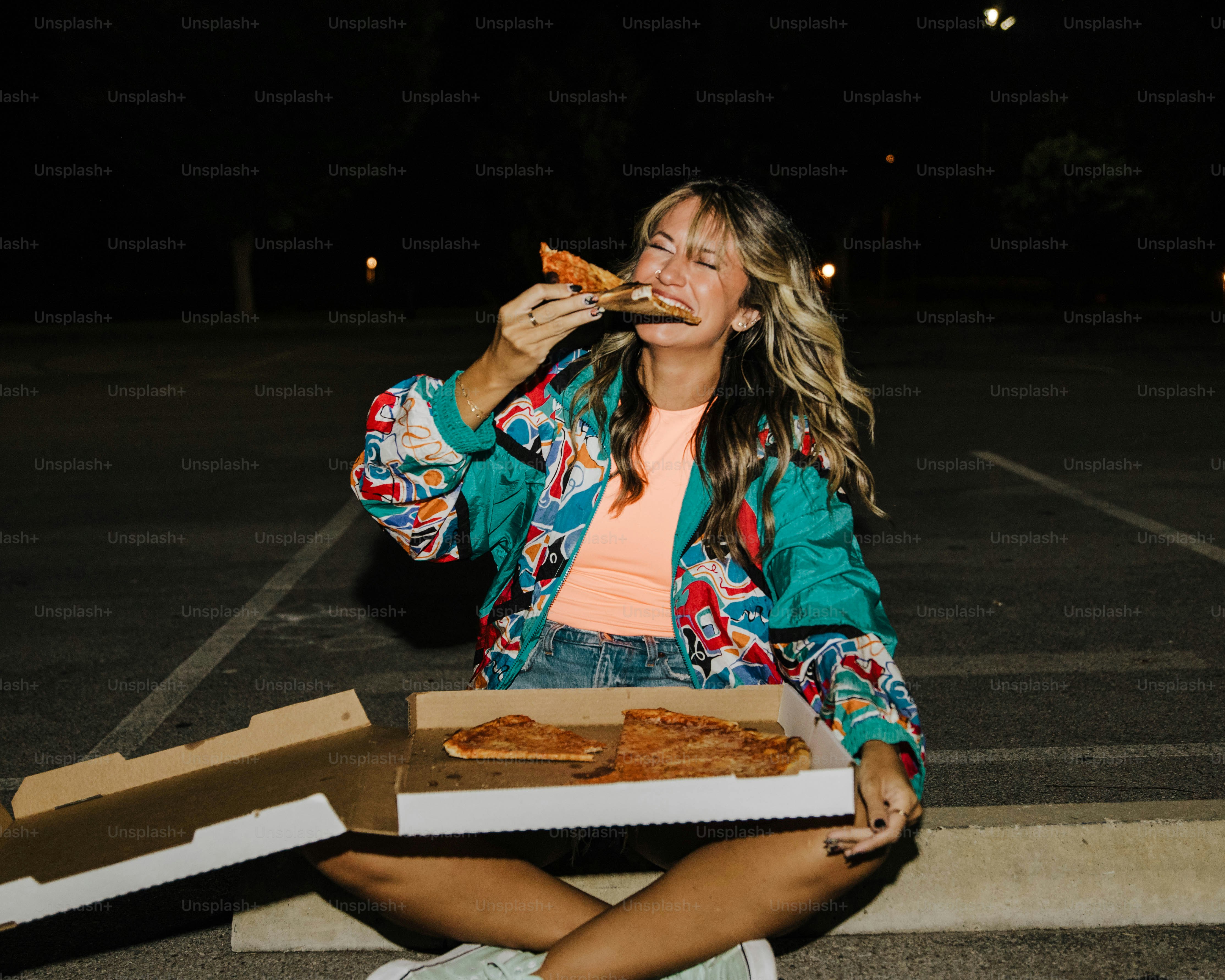 A woman sitting on the ground eating a slice of pizza photo – Takeaway ...