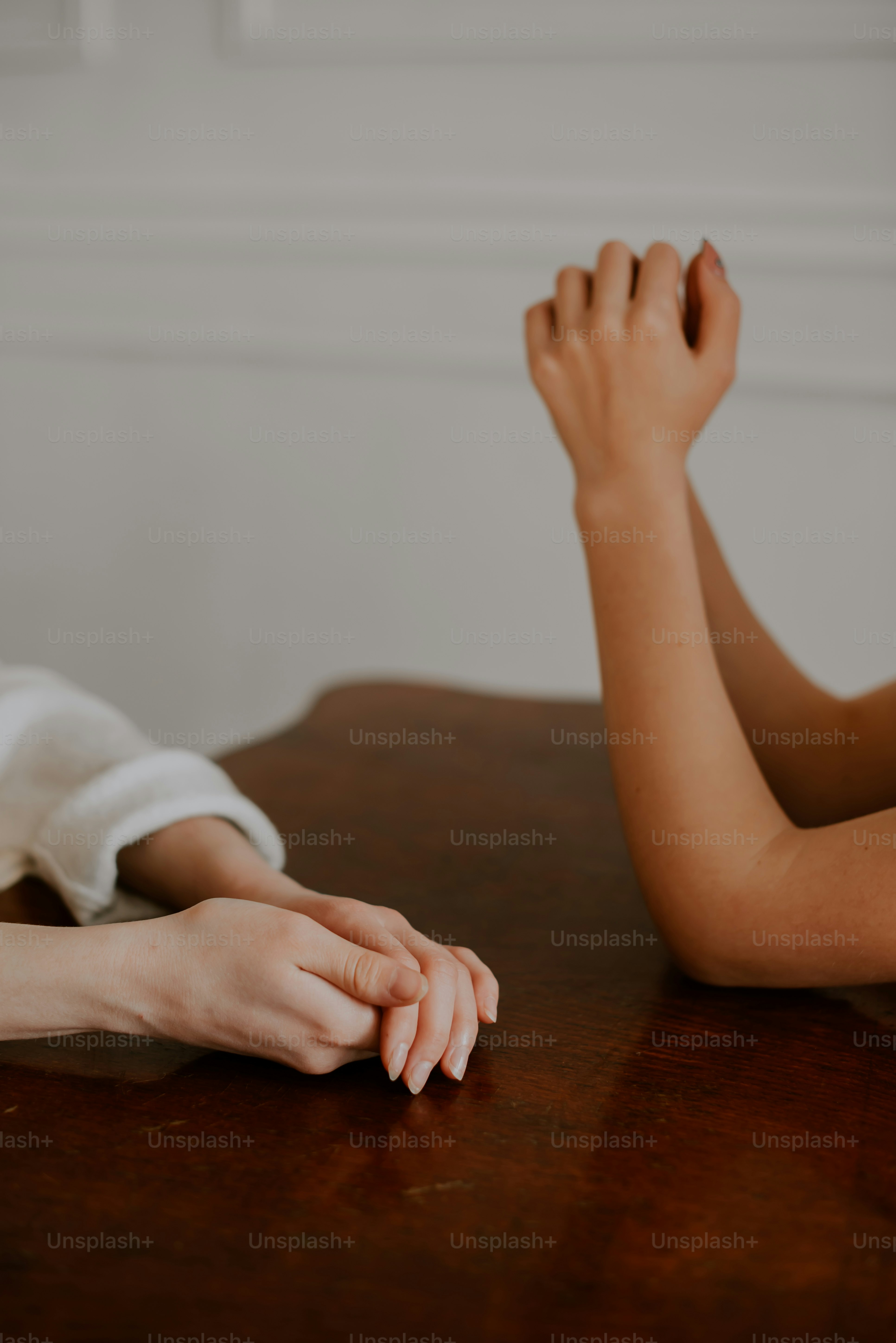 Two people sitting at a table with their hands on the table photo ...