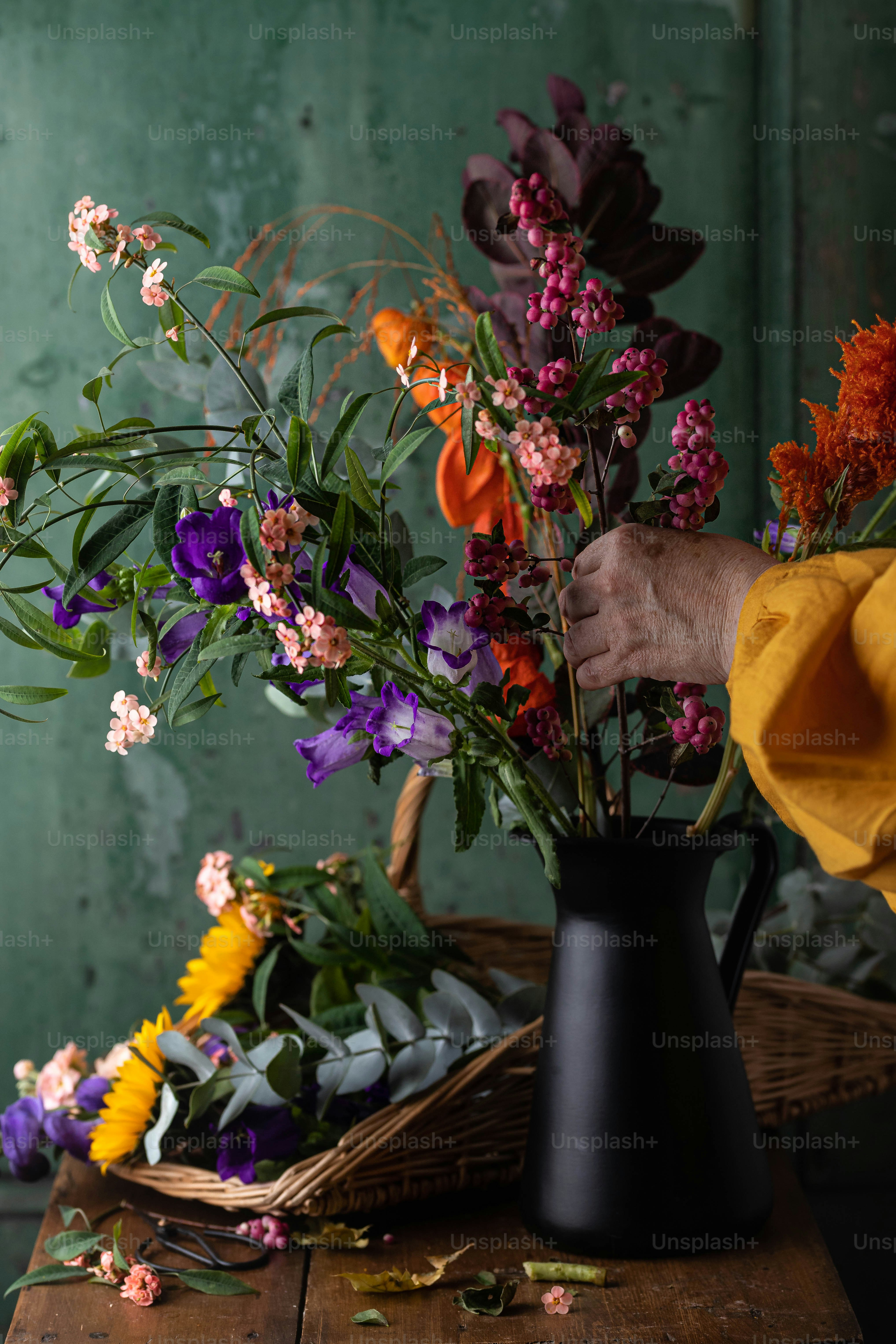 A person arranging flowers in a vase on a table photo – Flower ...