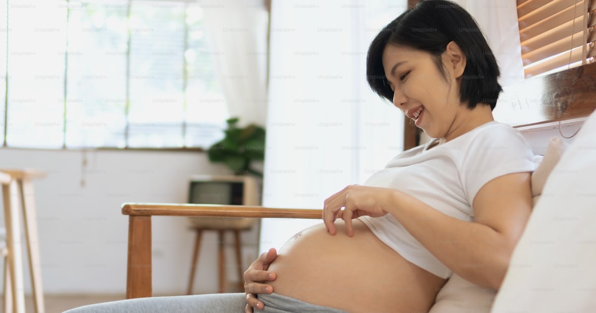 중국 또는 일본 여성 소파에 앉아 임신한 배를 연주 젊은 여자 기대 아기 그녀의 배를 만지고 사진 Unsplash의