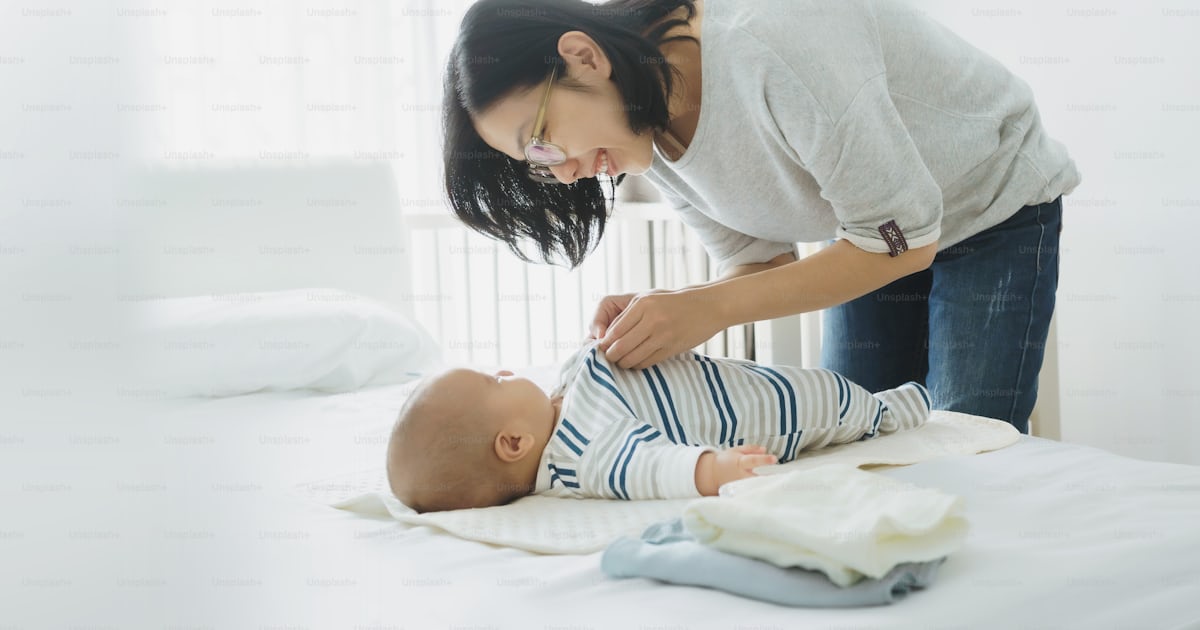 사랑하는 아시아 어머니는 집에서 침대에서 옷을 입히는 동안 작고 귀여운 아기와 놀고 있습니다 사진 Unsplash의 육아의