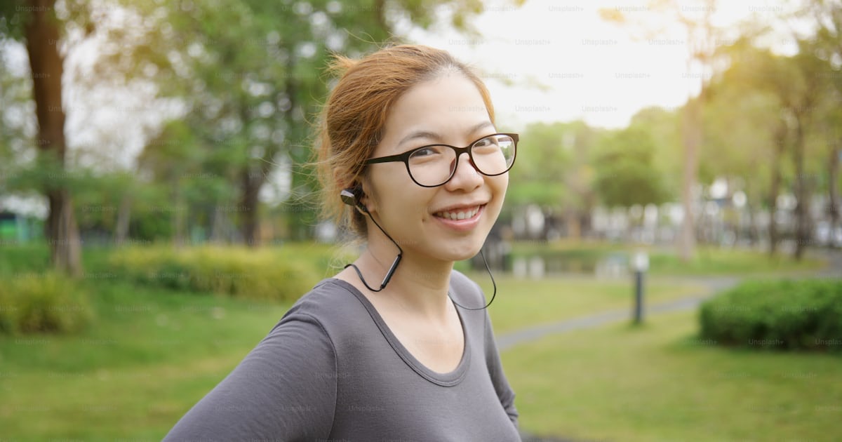 회색 운동복을 입은 행복한 젊은 아시아 여성은 아침에 야외에서 이어폰으로 음악을 들으며 웃고 있다 공원에서 여성 운동 건강