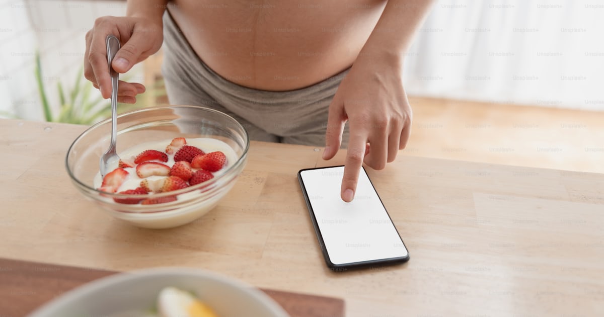 건강 식품을 먹으면서 휴대 전화를 사용하는 임산부 아시아 여성은 부엌에서 임신 중에 스마트폰 화면을 만지고 있다 사진