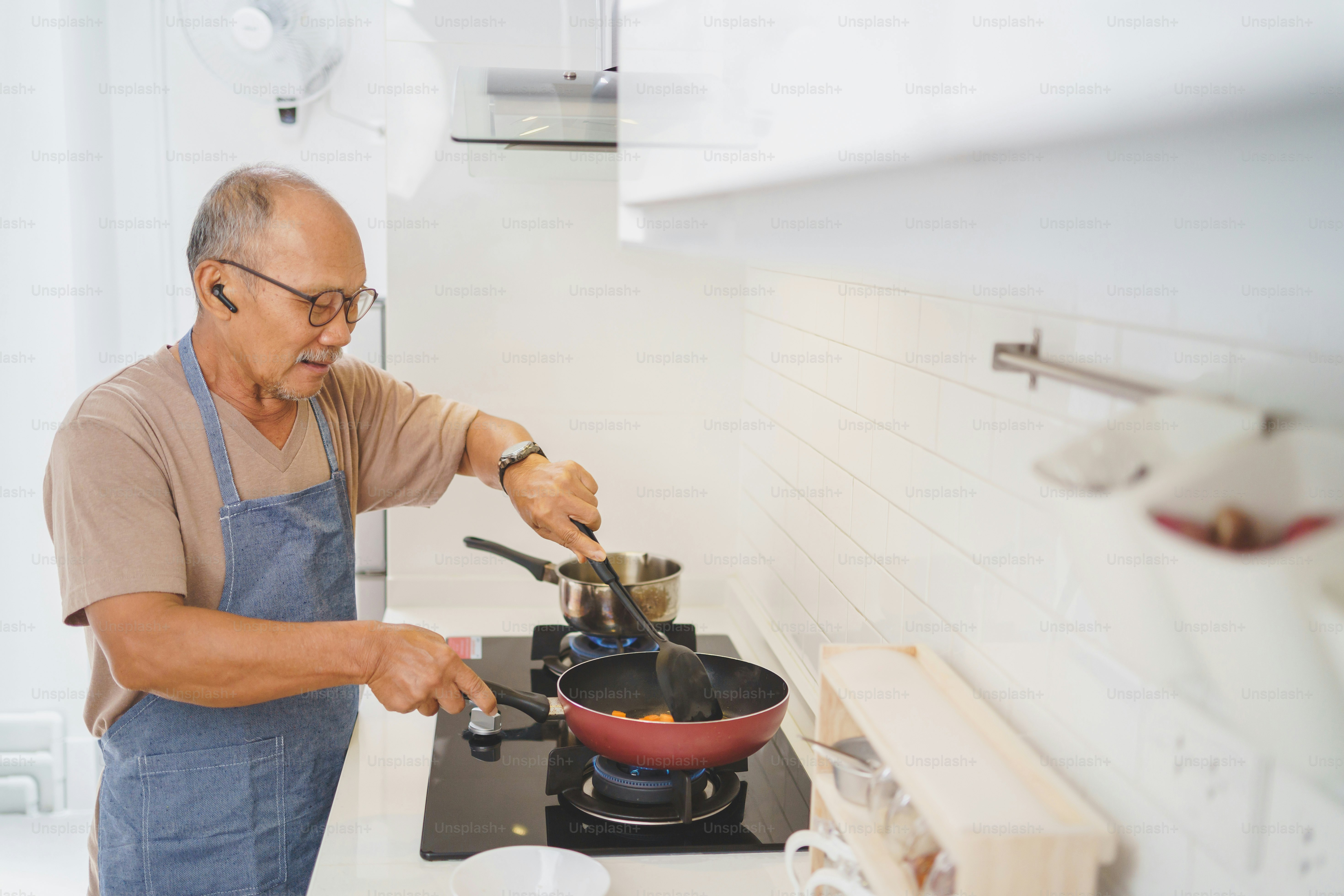 Happy Asian Mature adult man wearing eyeglasses cooking in kitchen ...
