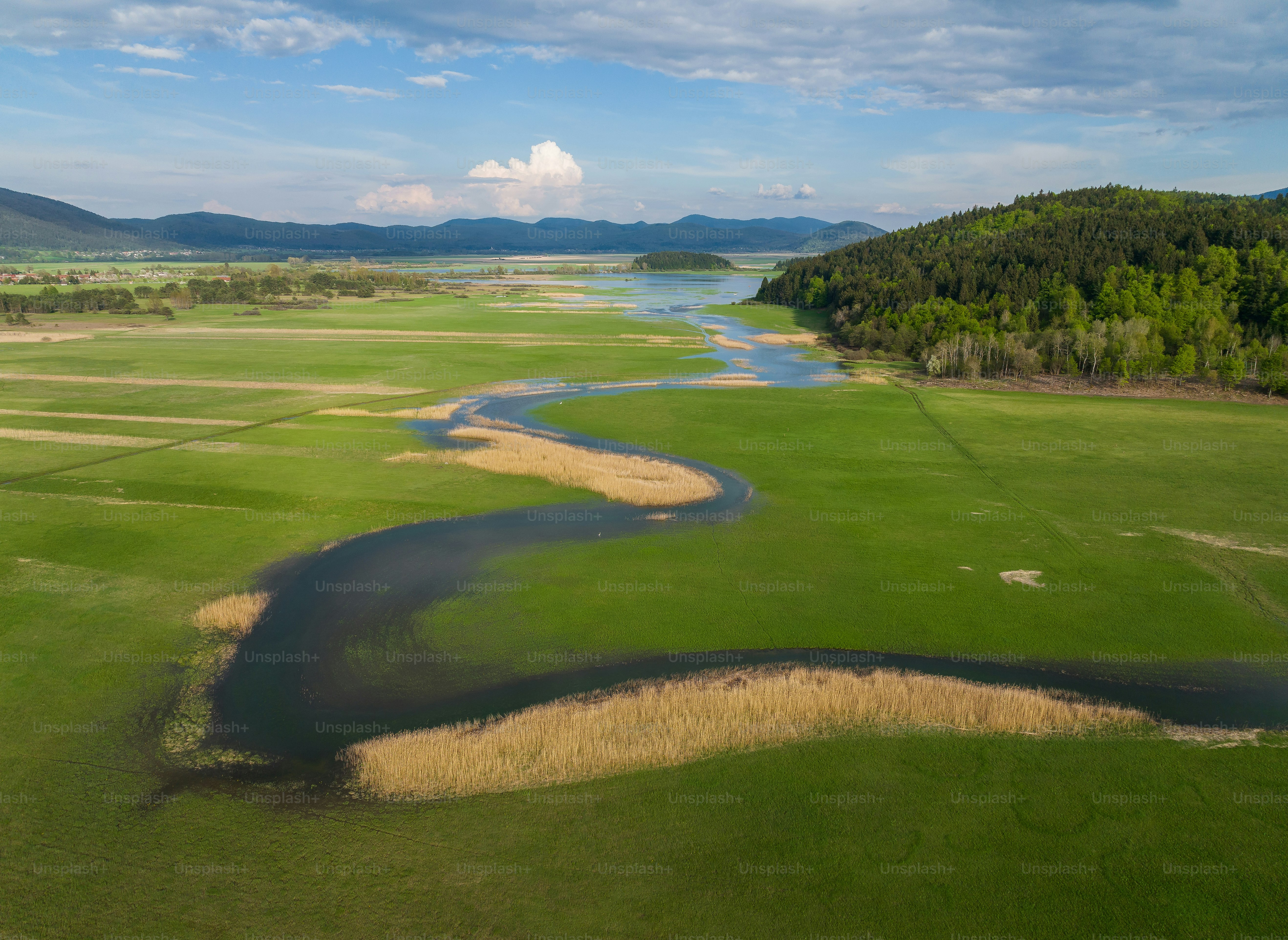 A wide open field with a river running through it photo – Clouds Image ...