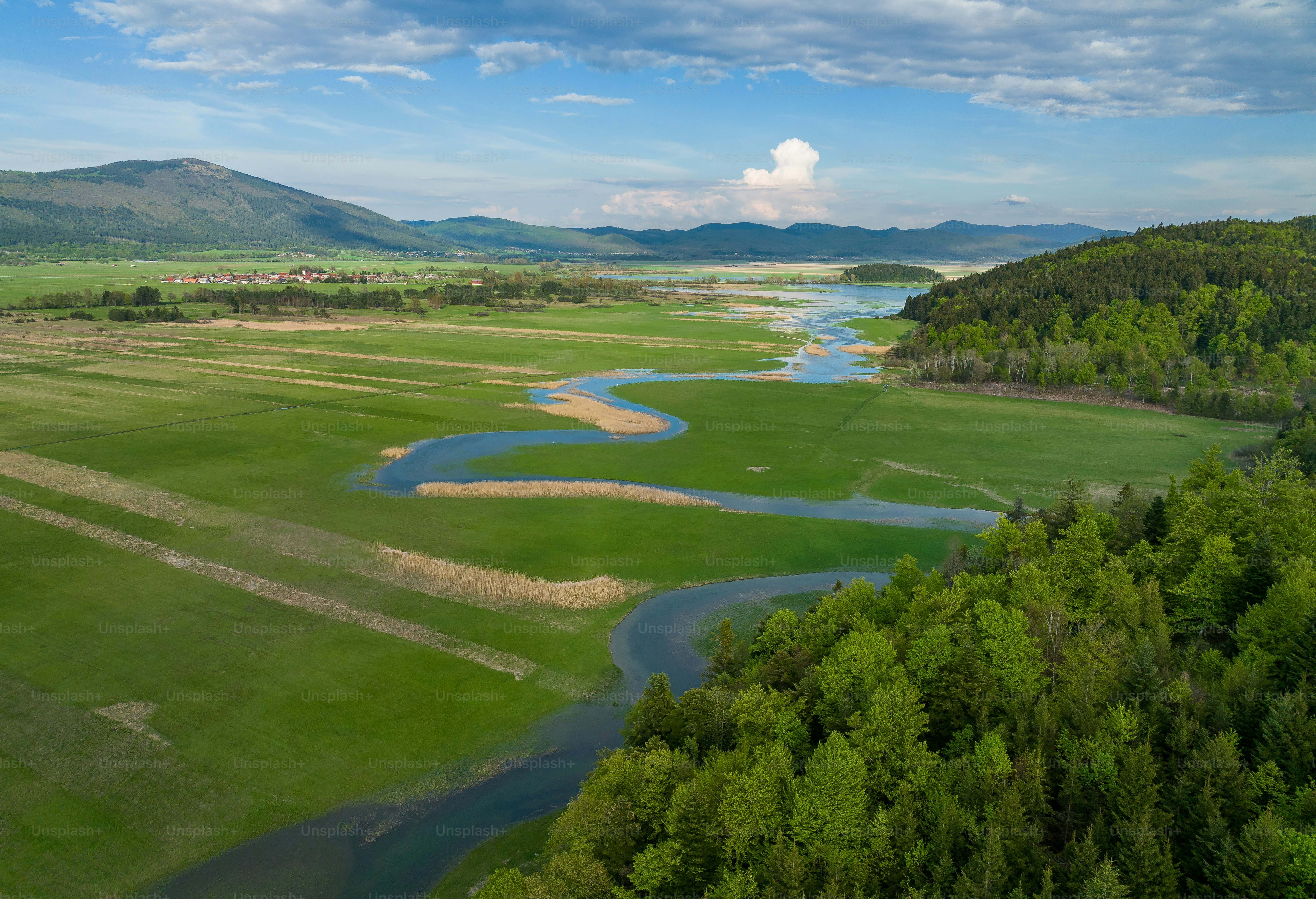 A wide open field with a river running through it photo – Clouds Image ...