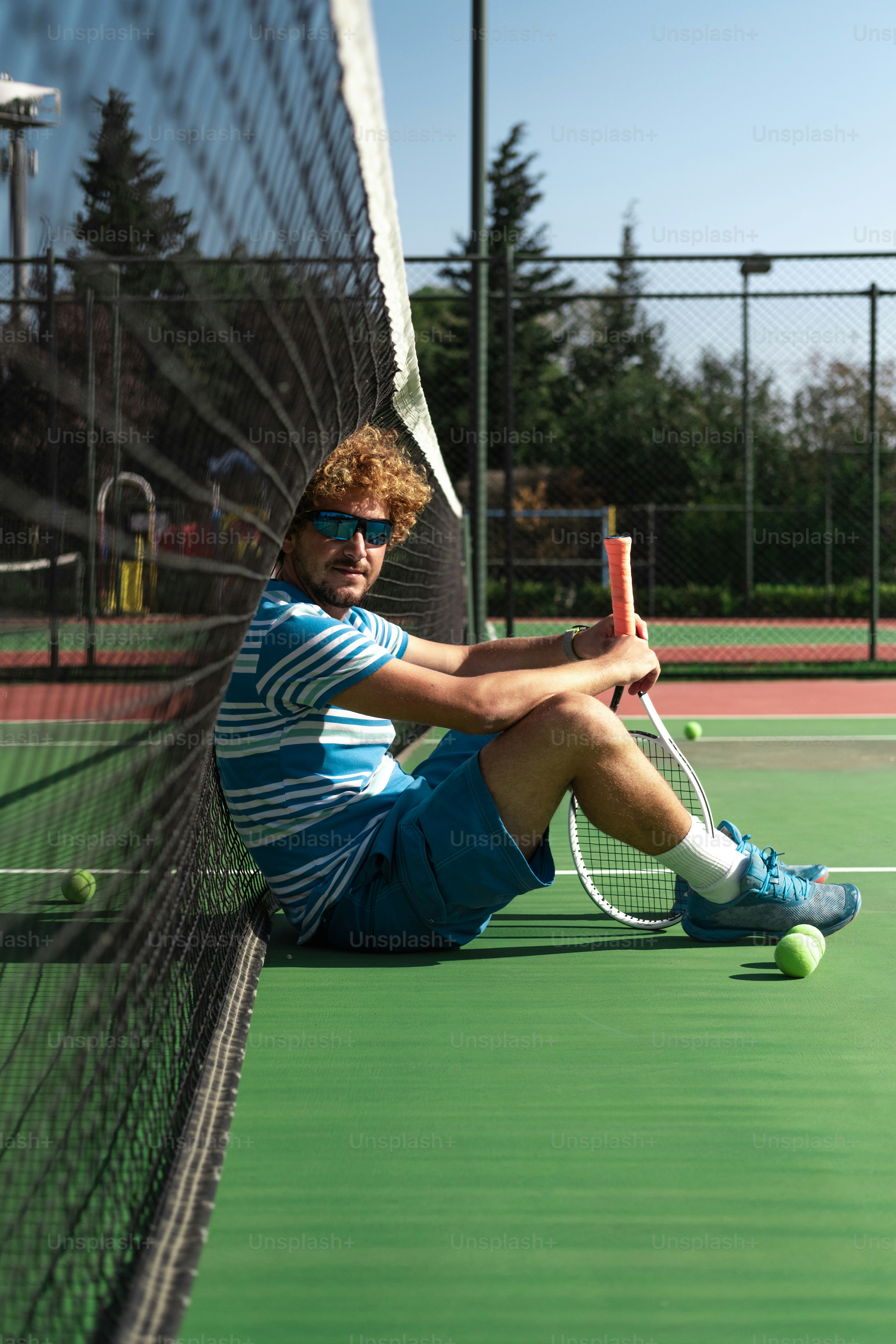 A man sitting on a tennis court holding a racquet photo – Tennis racket ...